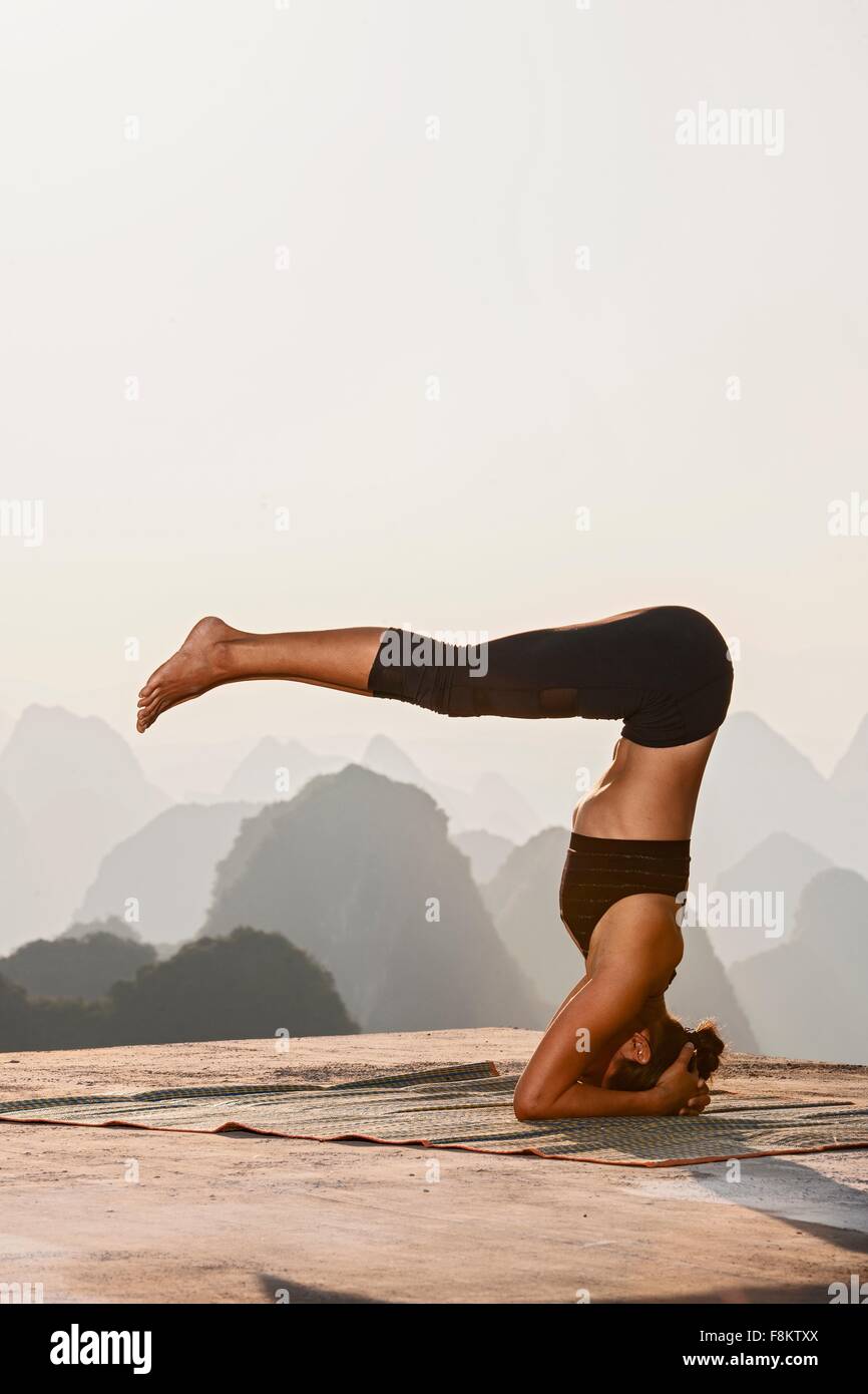 Side view of woman in headstand yoga pose above limestone mountains ...