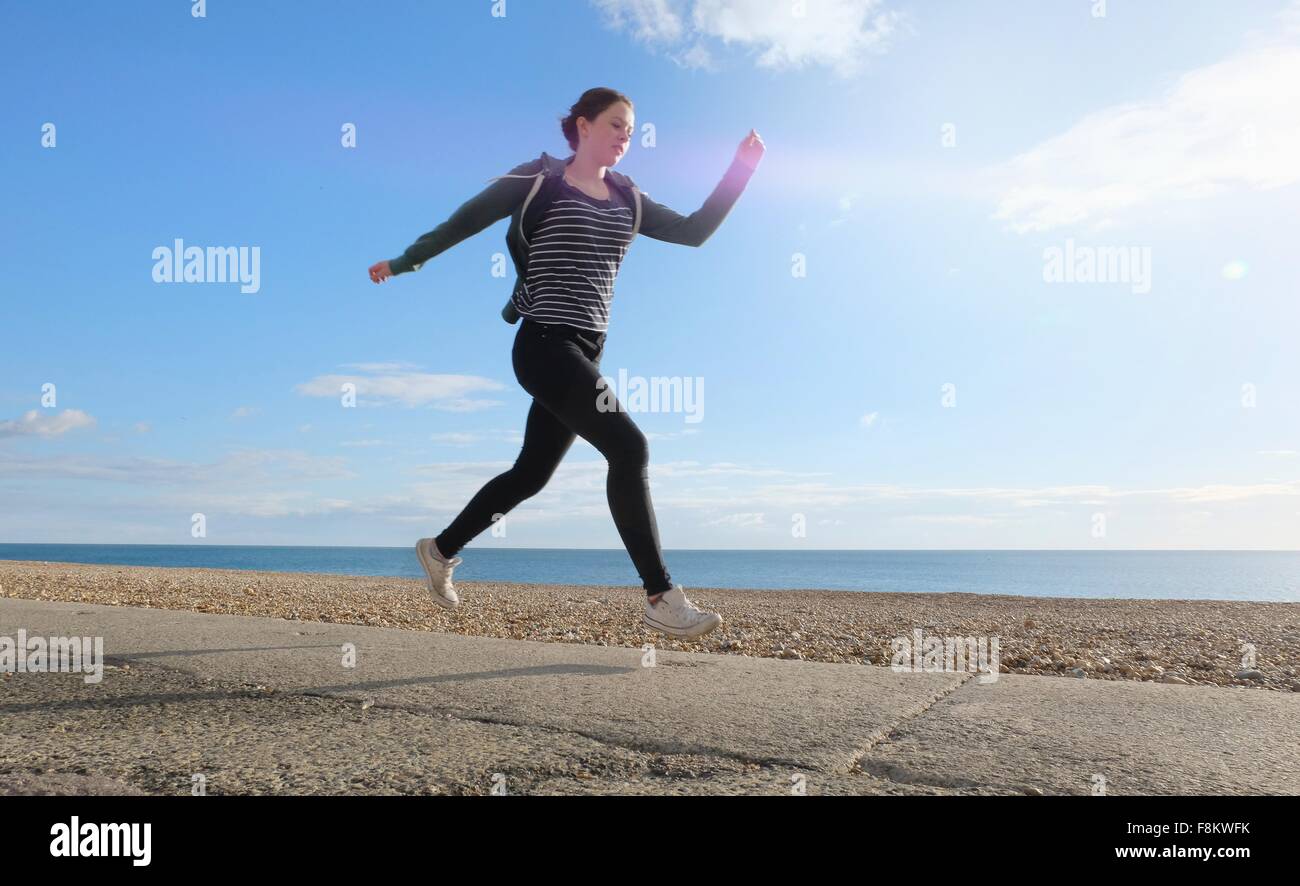 Young woman running along path on shingle beach Stock Photo - Alamy