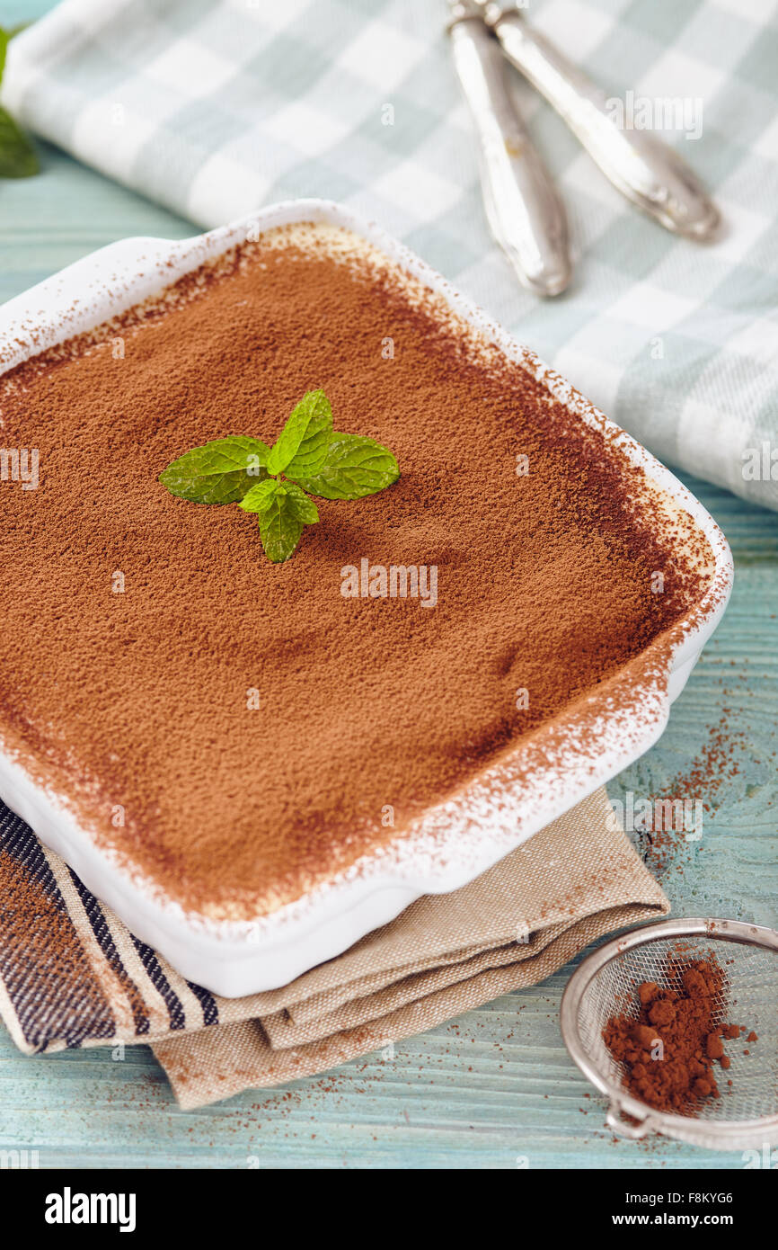 Tiramisu cake in an oven pan on a blue wooden table with dishes and ...