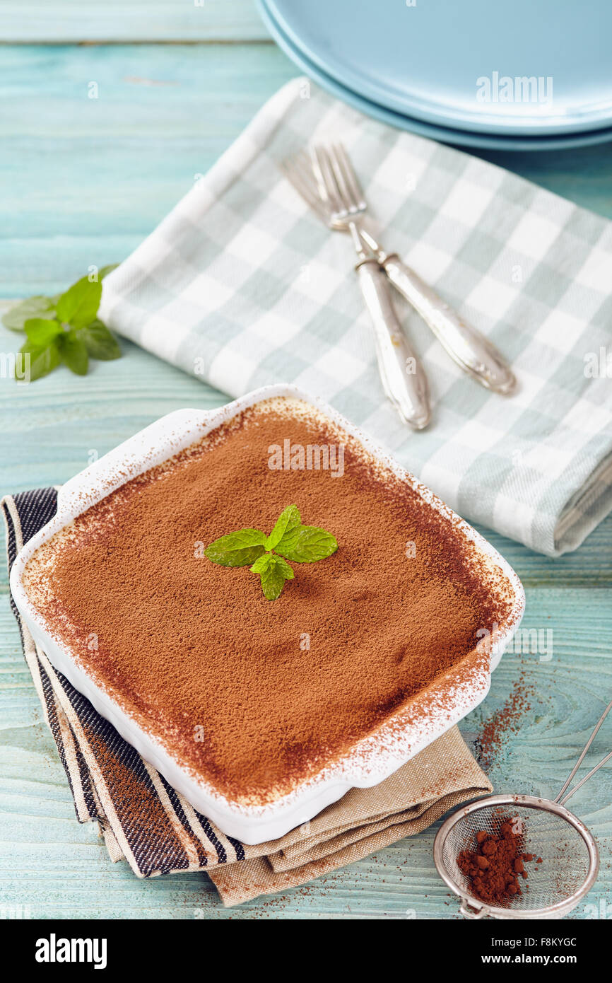 Tiramisu cake in an oven pan on a blue wooden table with dishes and ...