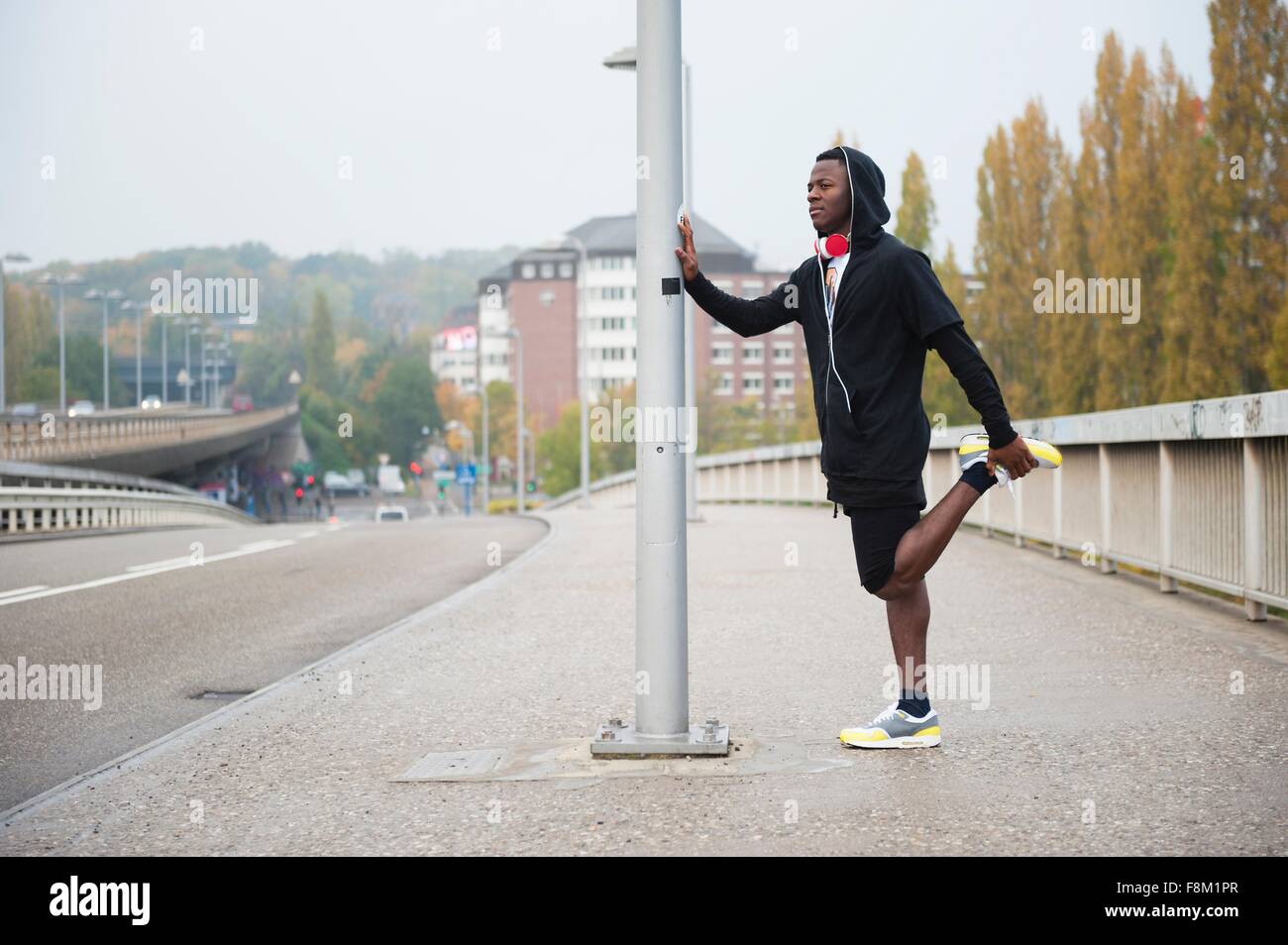 Young man leaning against lamppost, stretching Stock Photo - Alamy