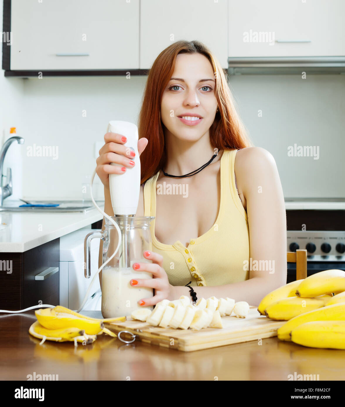 Young woman making beverages with blender from bananas and milk at ...