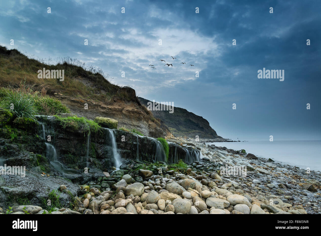 Landscape image of waterfall flowing onto rocky beach at sunrise Stock ...