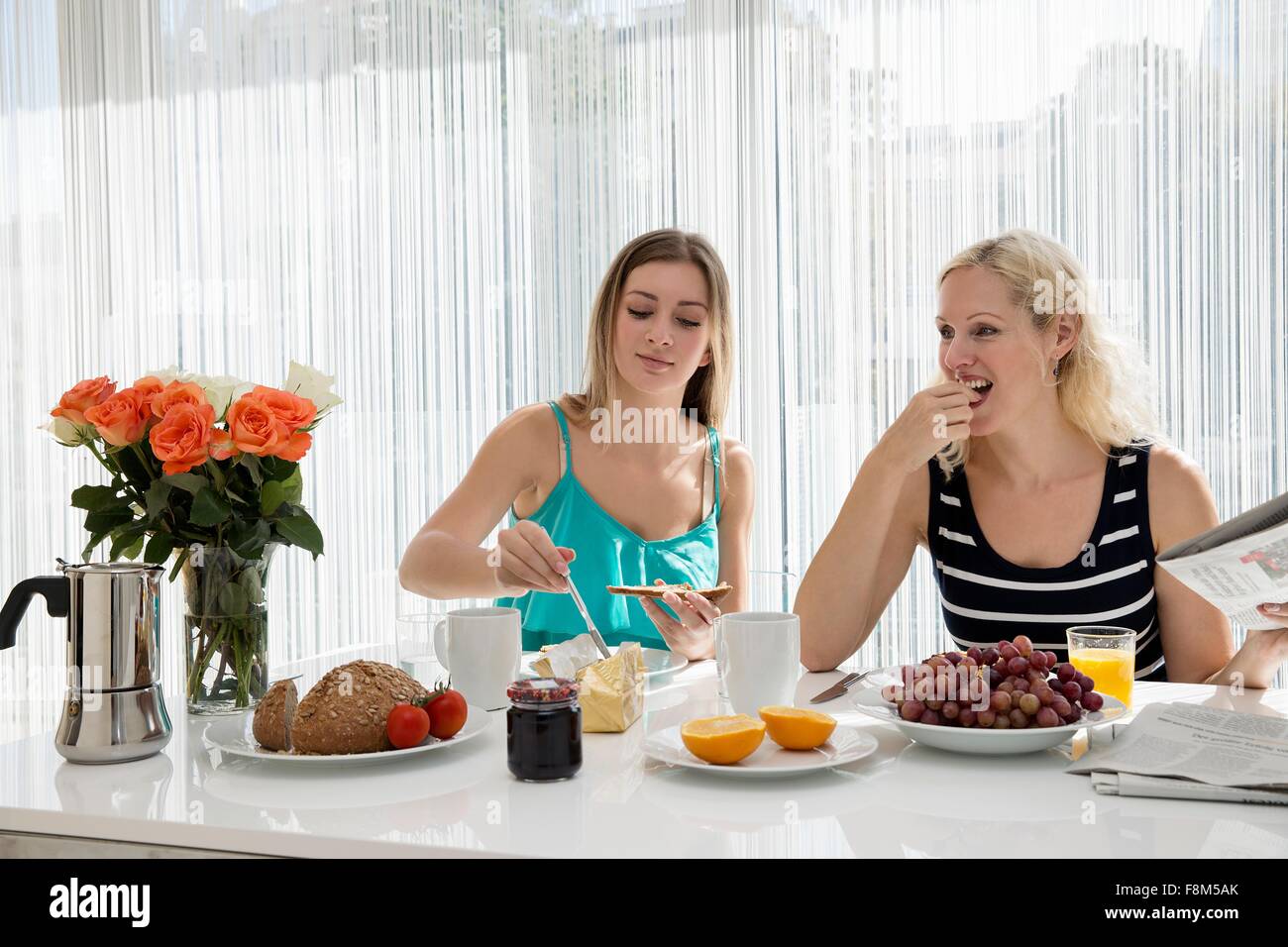 Women sitting at dining table spreading butter on bread, eating a ...