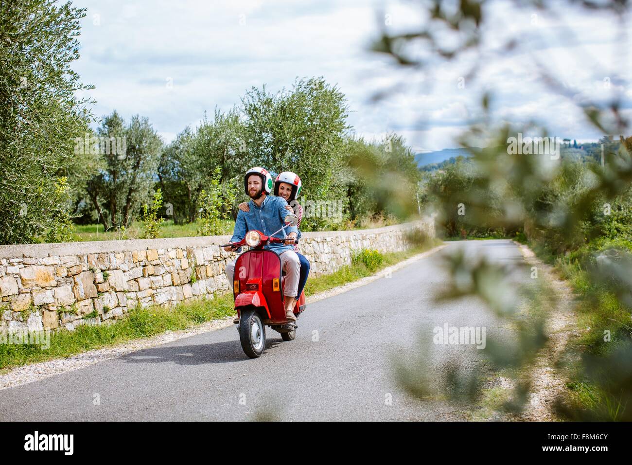 Young couple riding moped past olive grove, Florence, Italy Stock Photo ...