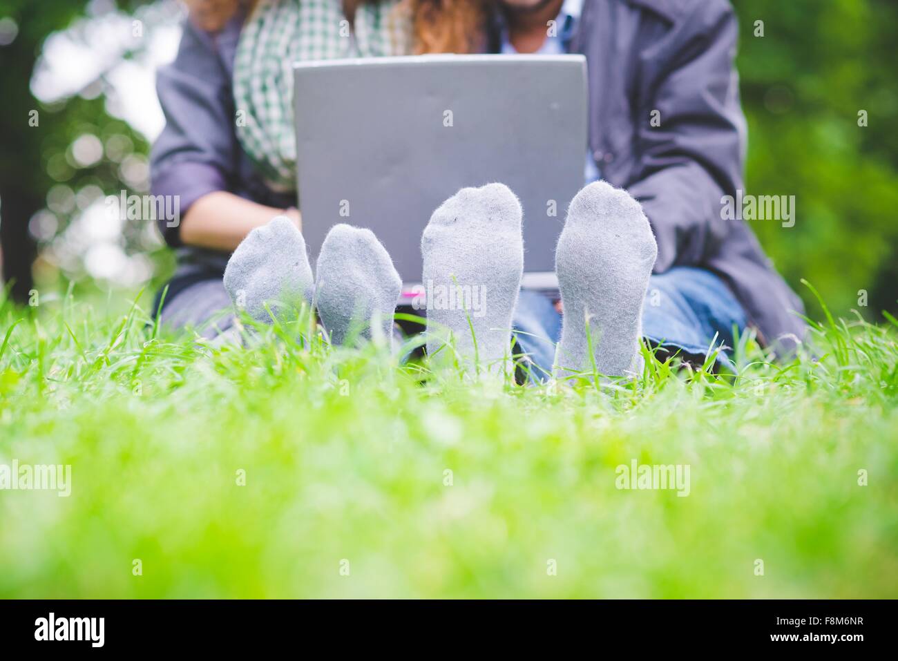 Feet of young couple wearing socks sitting on grass using laptop ...