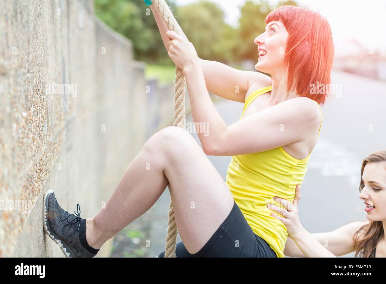Young women climbing over wall with rope Stock Photo - Alamy