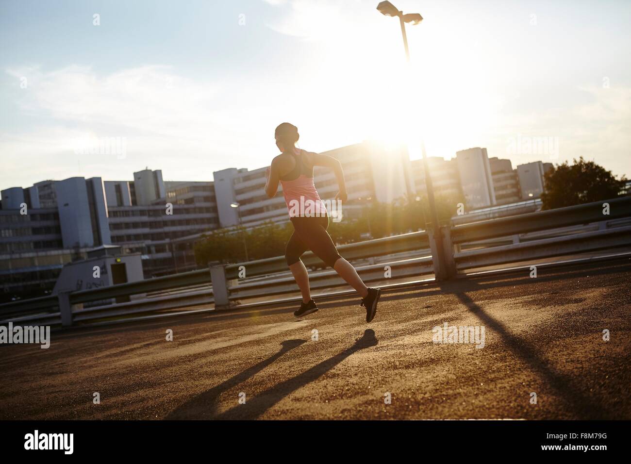 Sunlit silhouette of young female runner running on rooftop Stock Photo ...