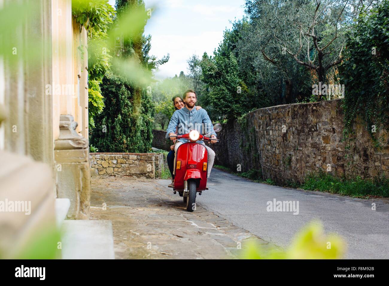 Young couple riding moped through village, Florence, Italy Stock Photo ...