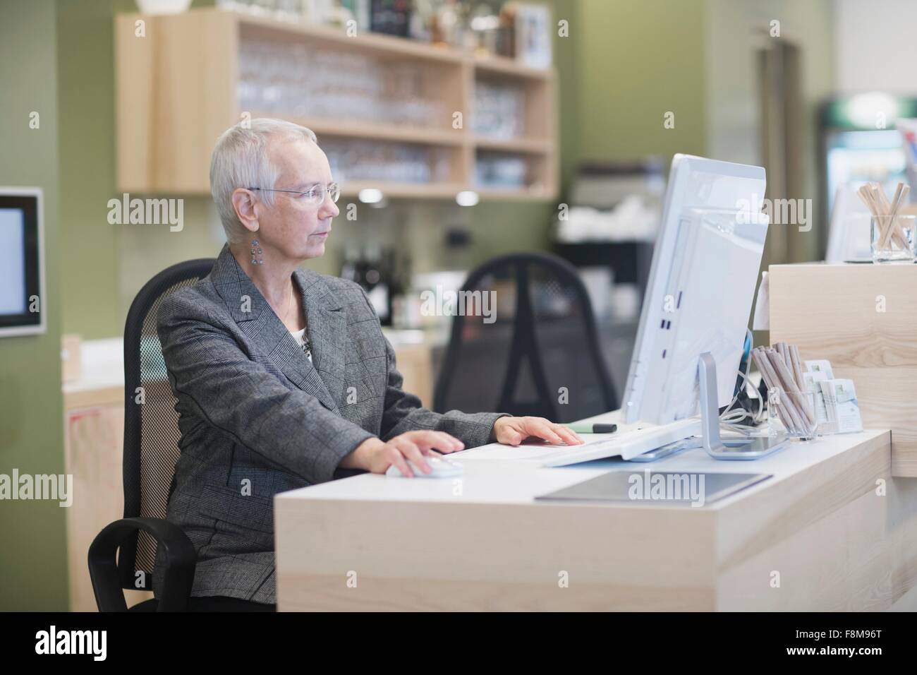 Senior female receptionist using desktop computer at hotel reception ...