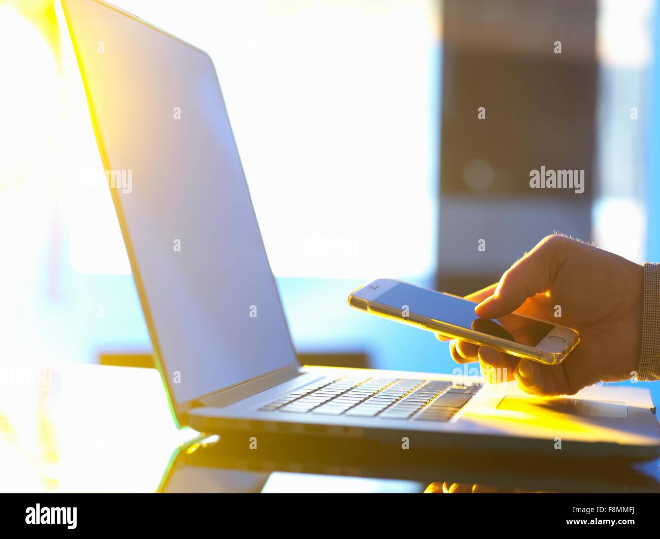Business man at laptop computer with smartphone in office with sunlight ...