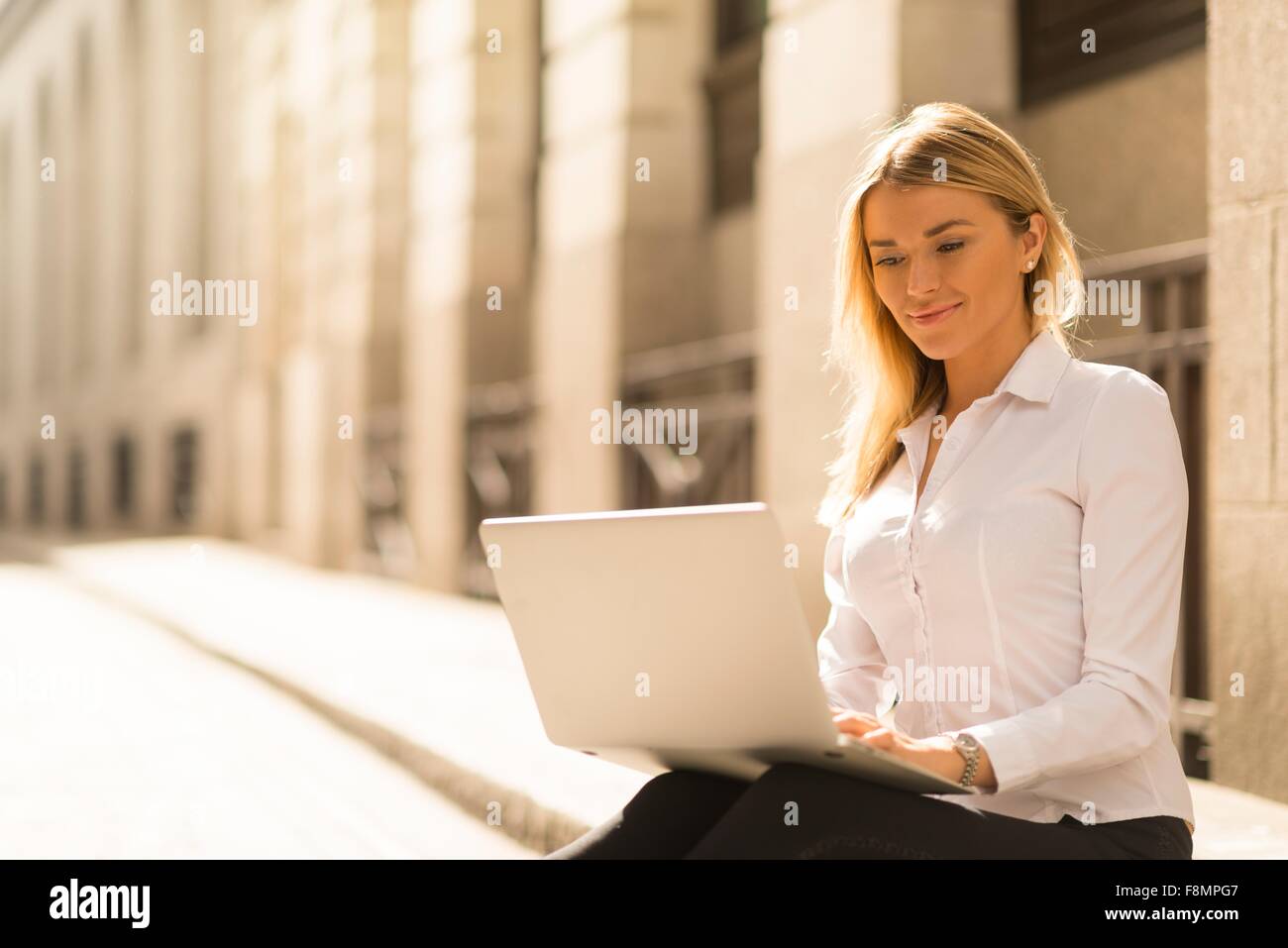 Businesswoman using laptop on kerb, London, UK Stock Photo - Alamy