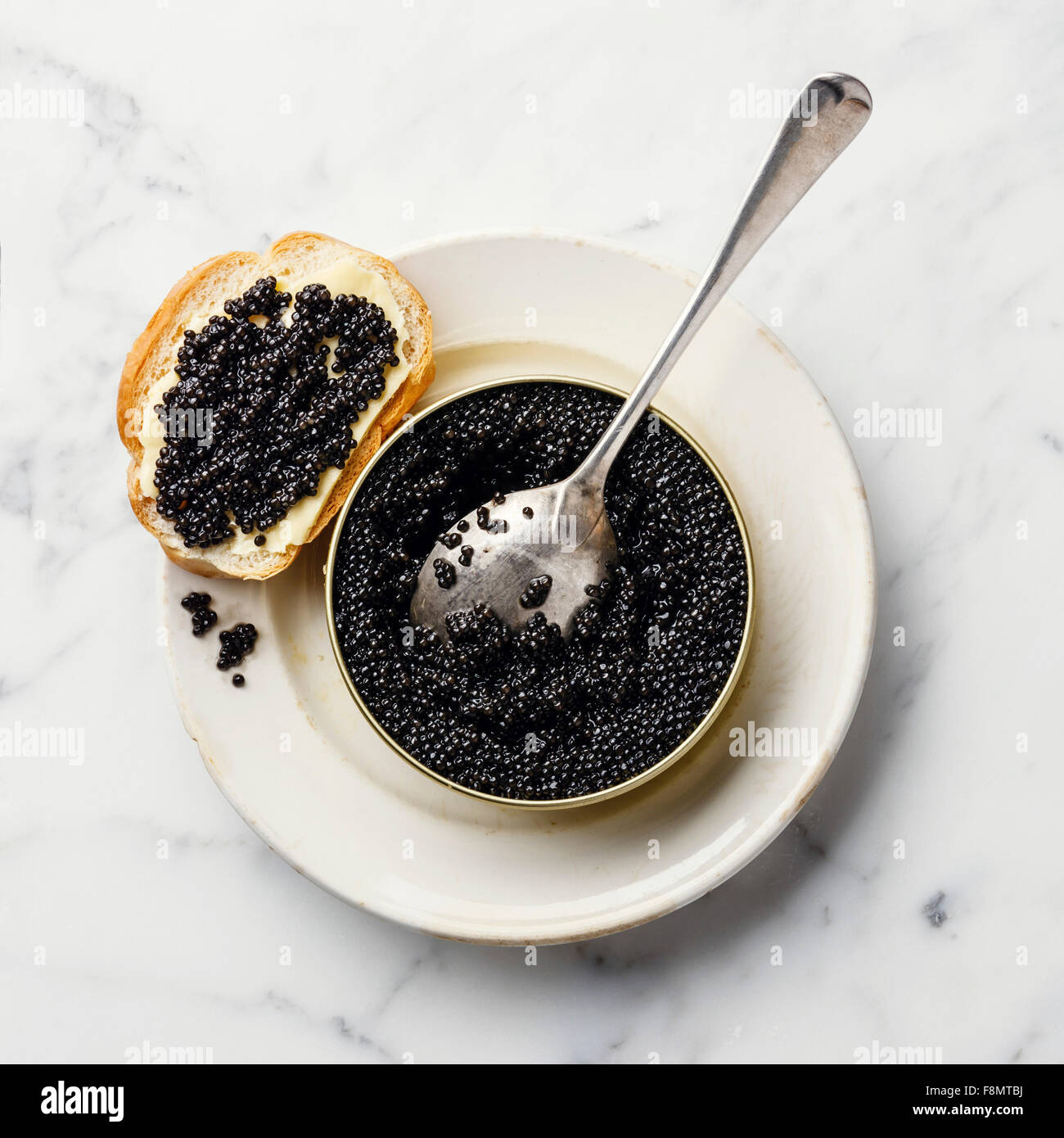 Sturgeon black caviar in can and sandwich on white marble background ...