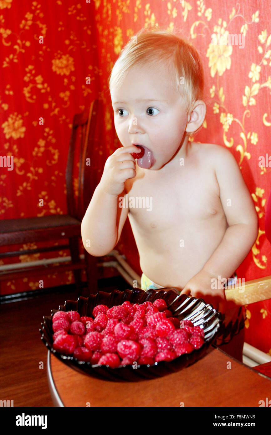 little baby eats raspberry in the red room Stock Photo - Alamy