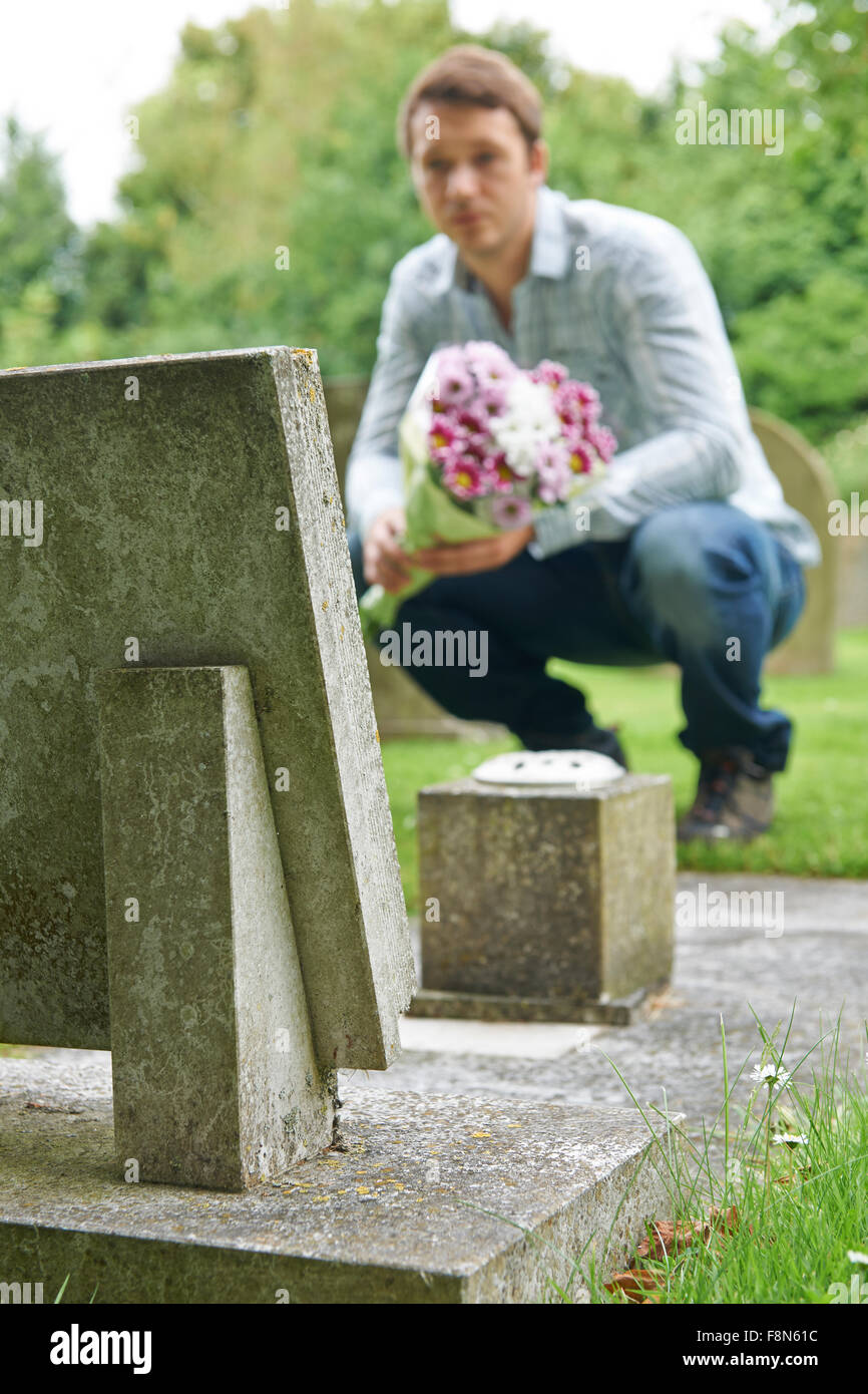 Man Placing Flowers By Headstone In Cemetery Stock Photo - Alamy