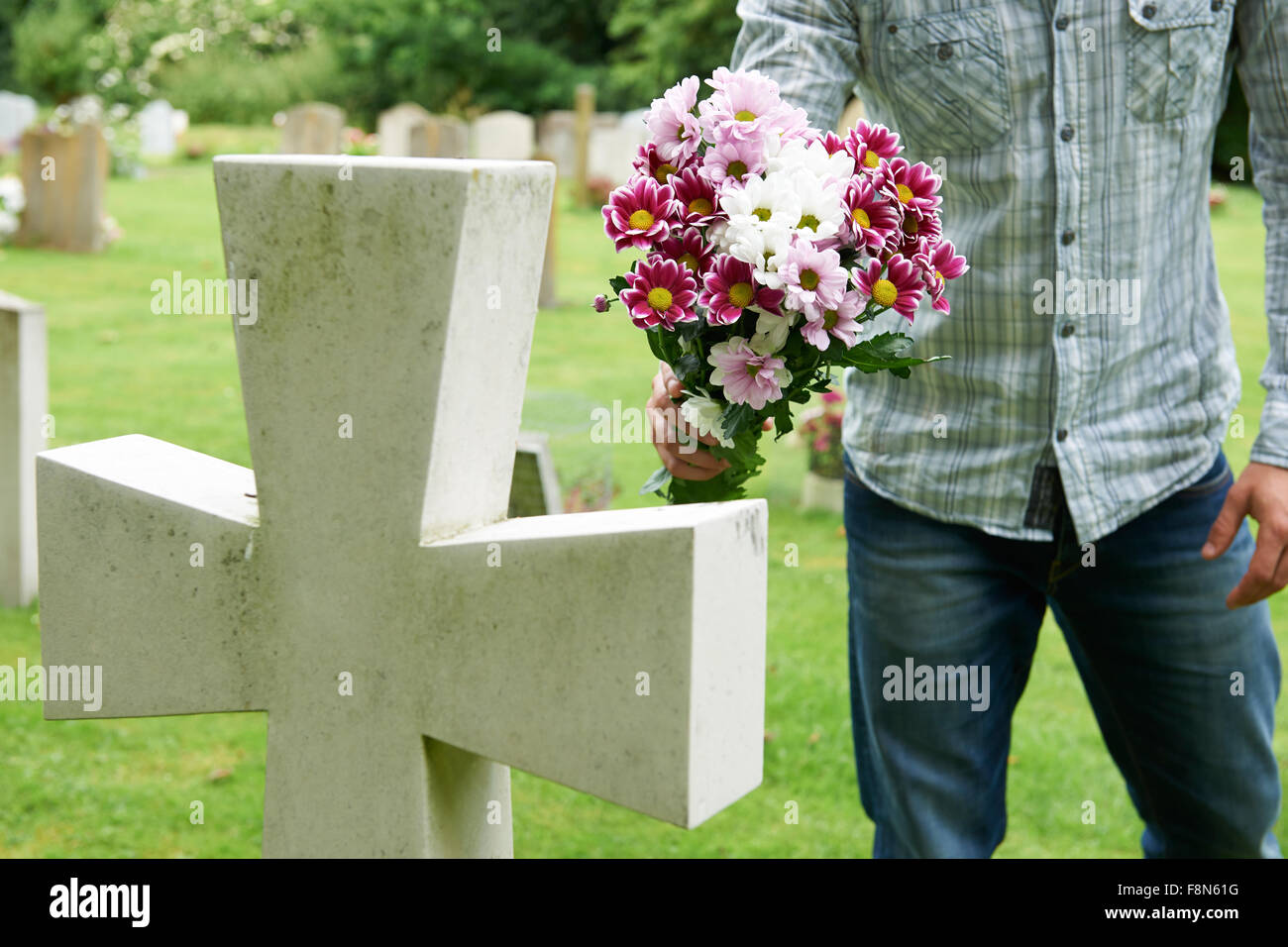 Man Placing Flowers By Headstone In Cemetery Stock Photo - Alamy