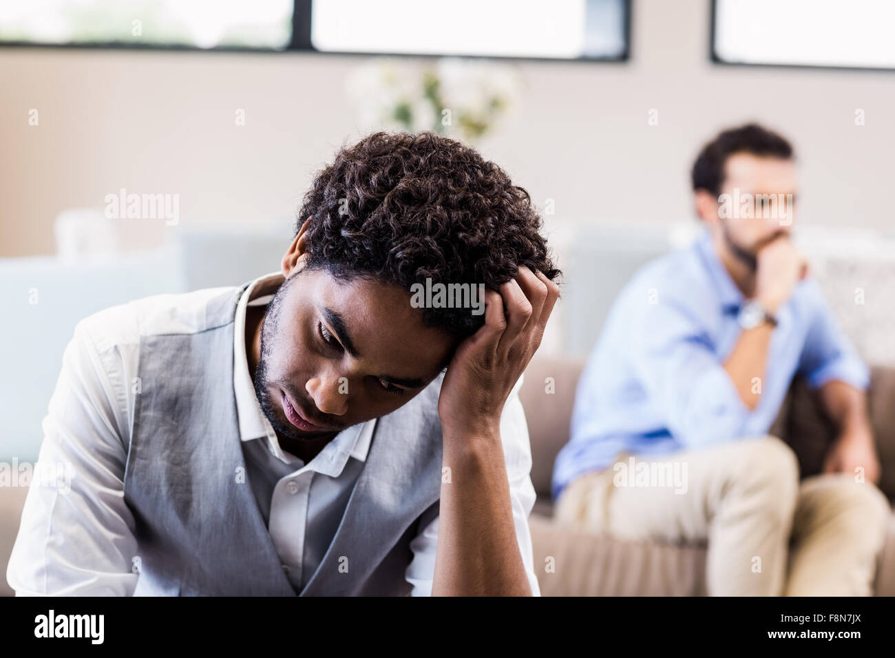 Troubled man sitting in foreground Stock Photo - Alamy