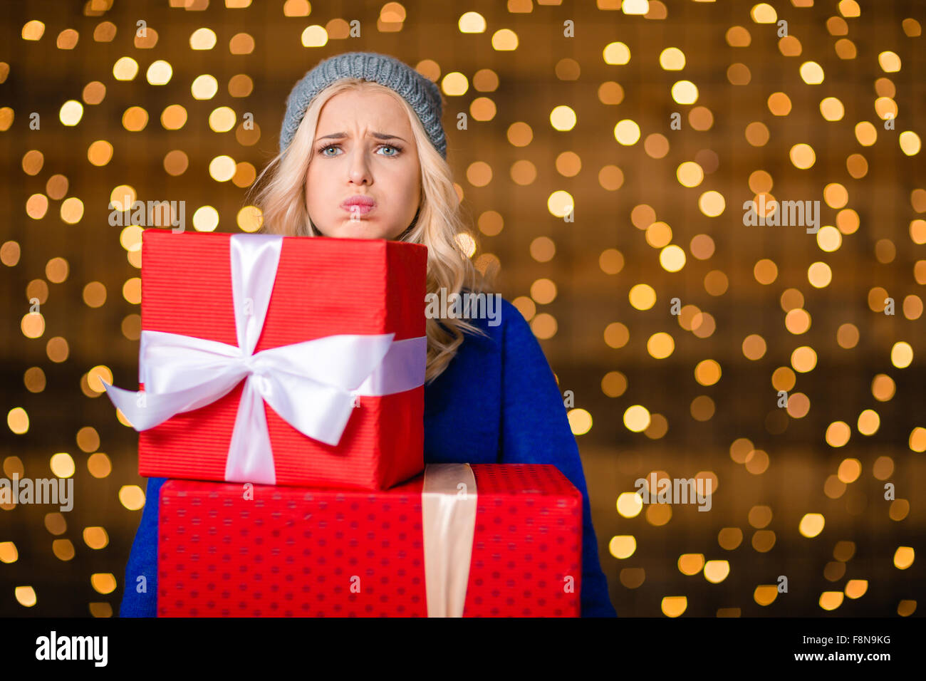 Portrait of a sad woman holding gift boxes over holidays lights ...