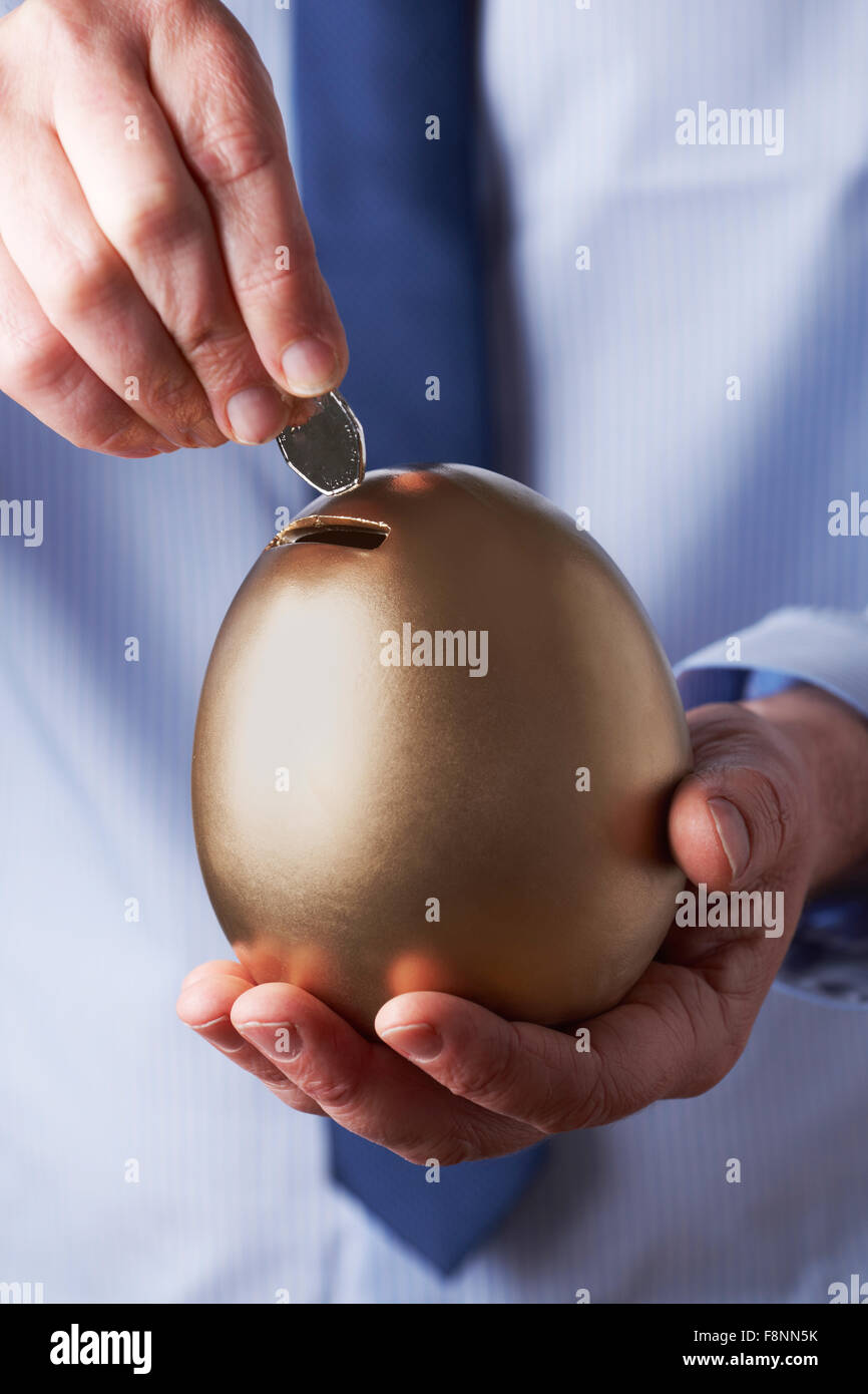 Businessman Putting Coin Into Egg Shaped Money Box Stock Photo - Alamy