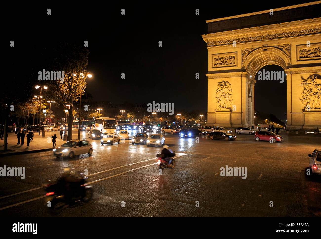 Cars drive around the base of the Arc de Triomphe at night in Paris ...