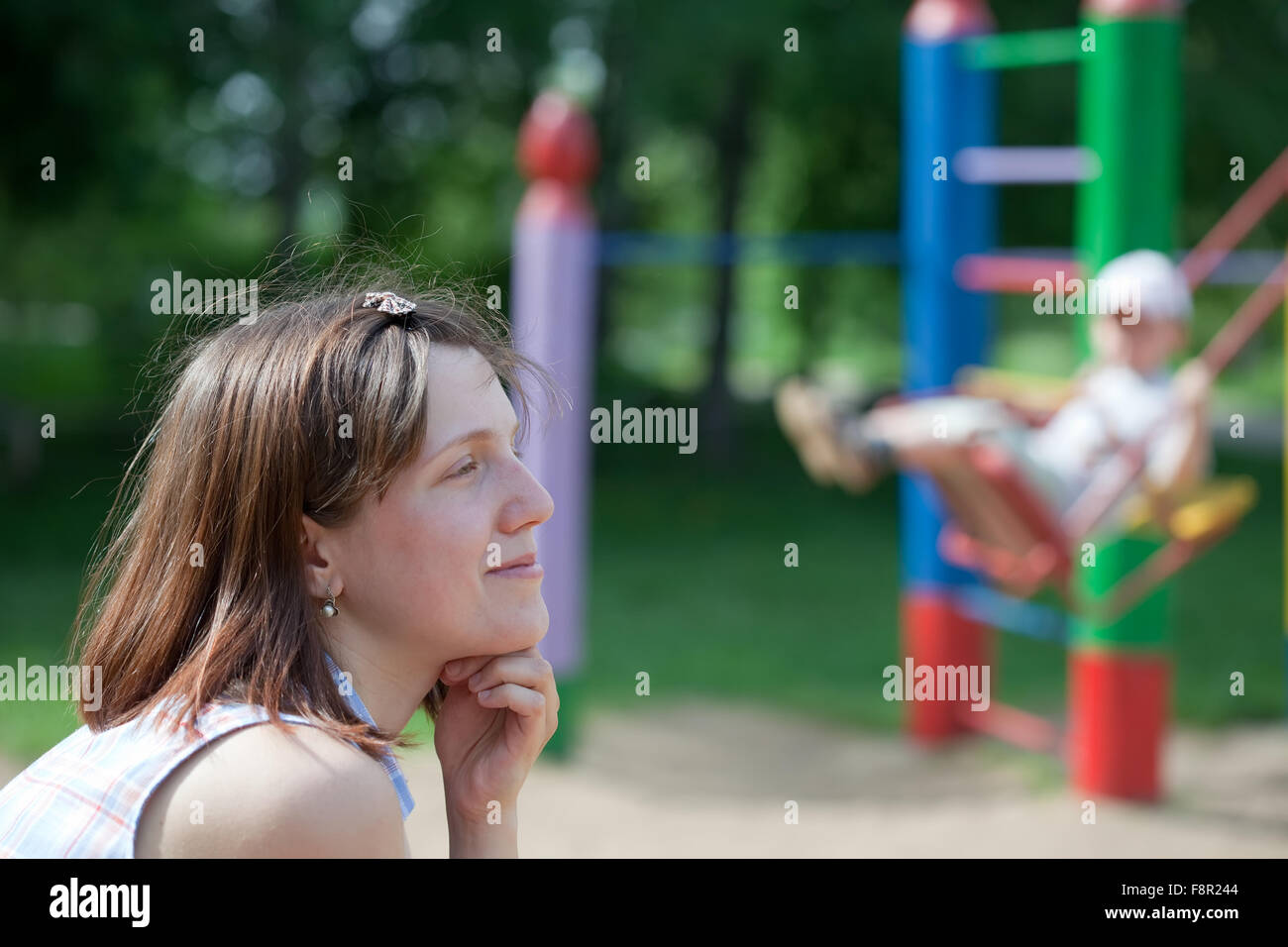 Portrait of woman against child on swings in playground Stock Photo - Alamy
