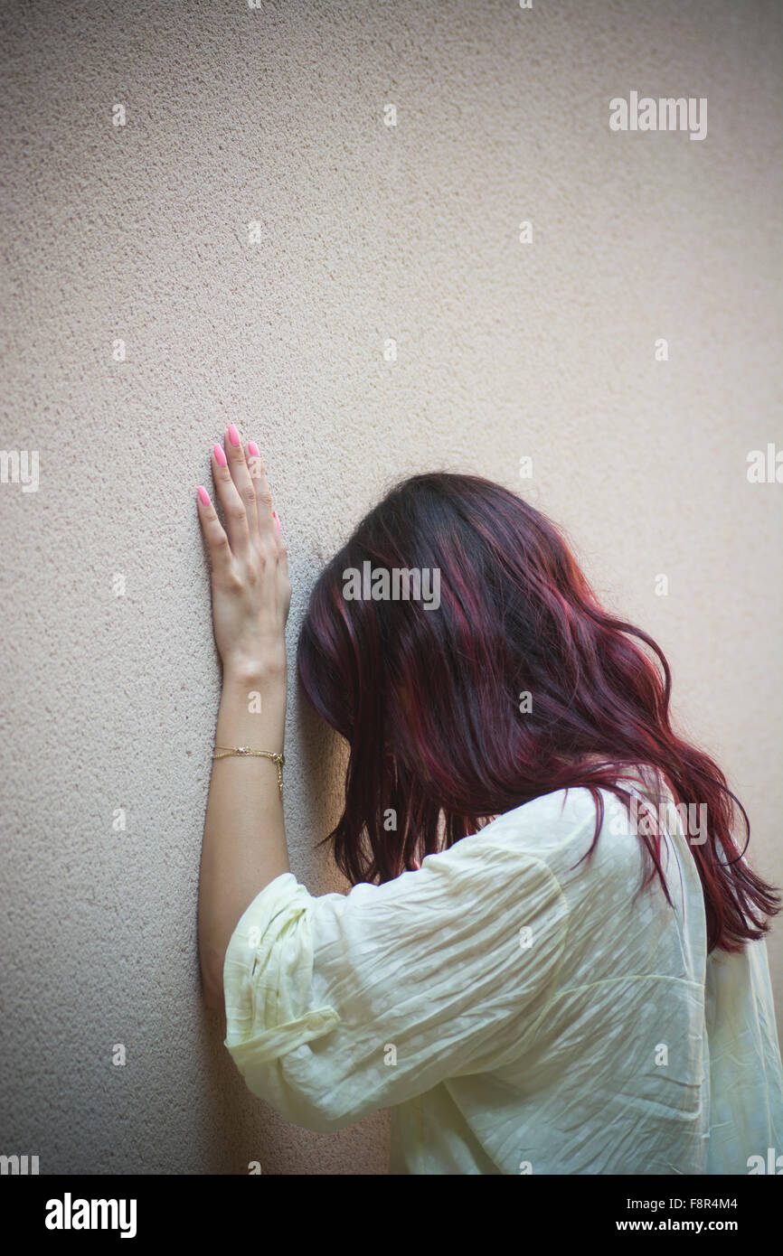 Miserable young woman with red hair leaning on the wall outdoors Stock ...