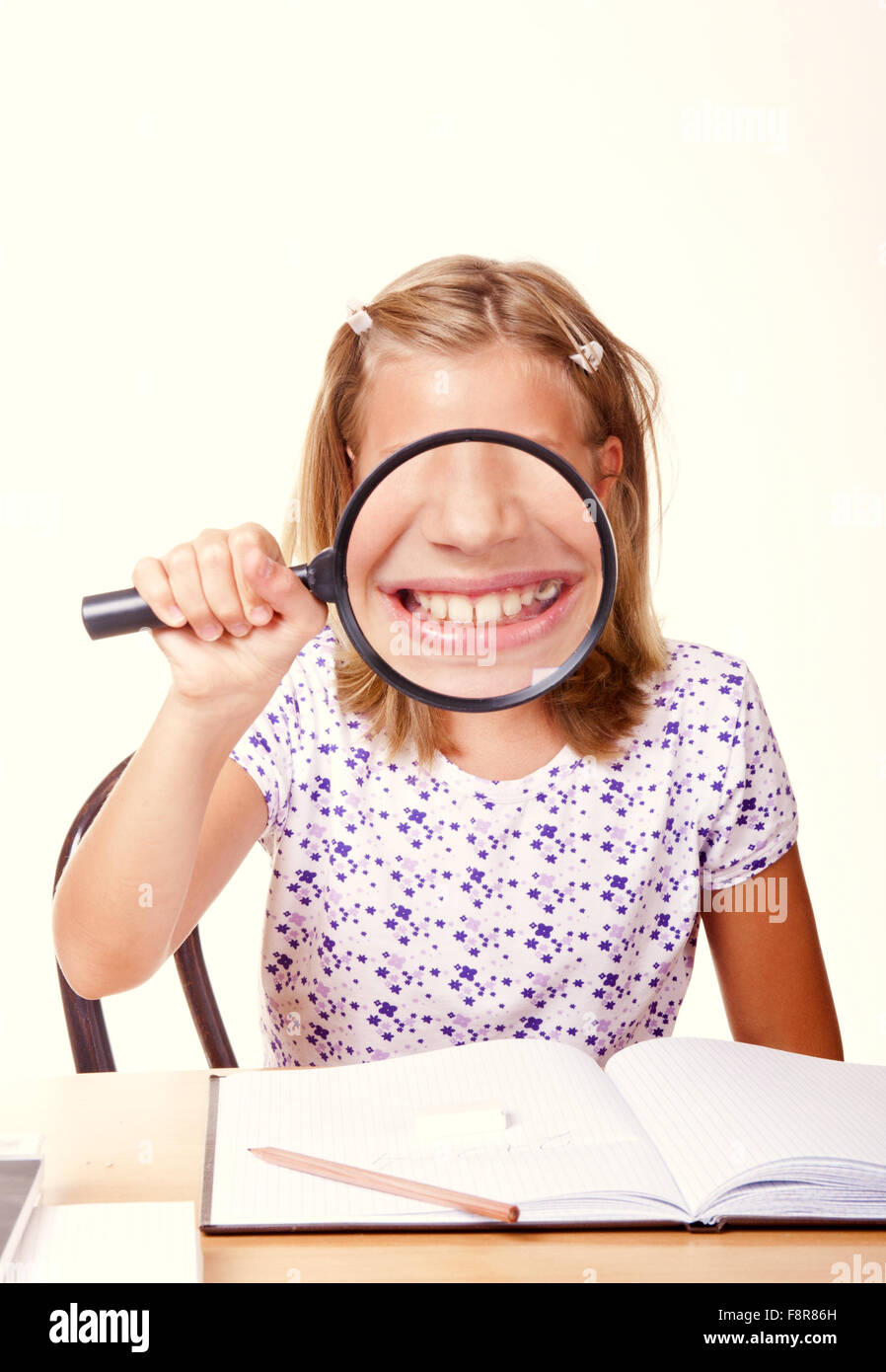 happy young school girl sit with a magnifying glass in hand and write ...