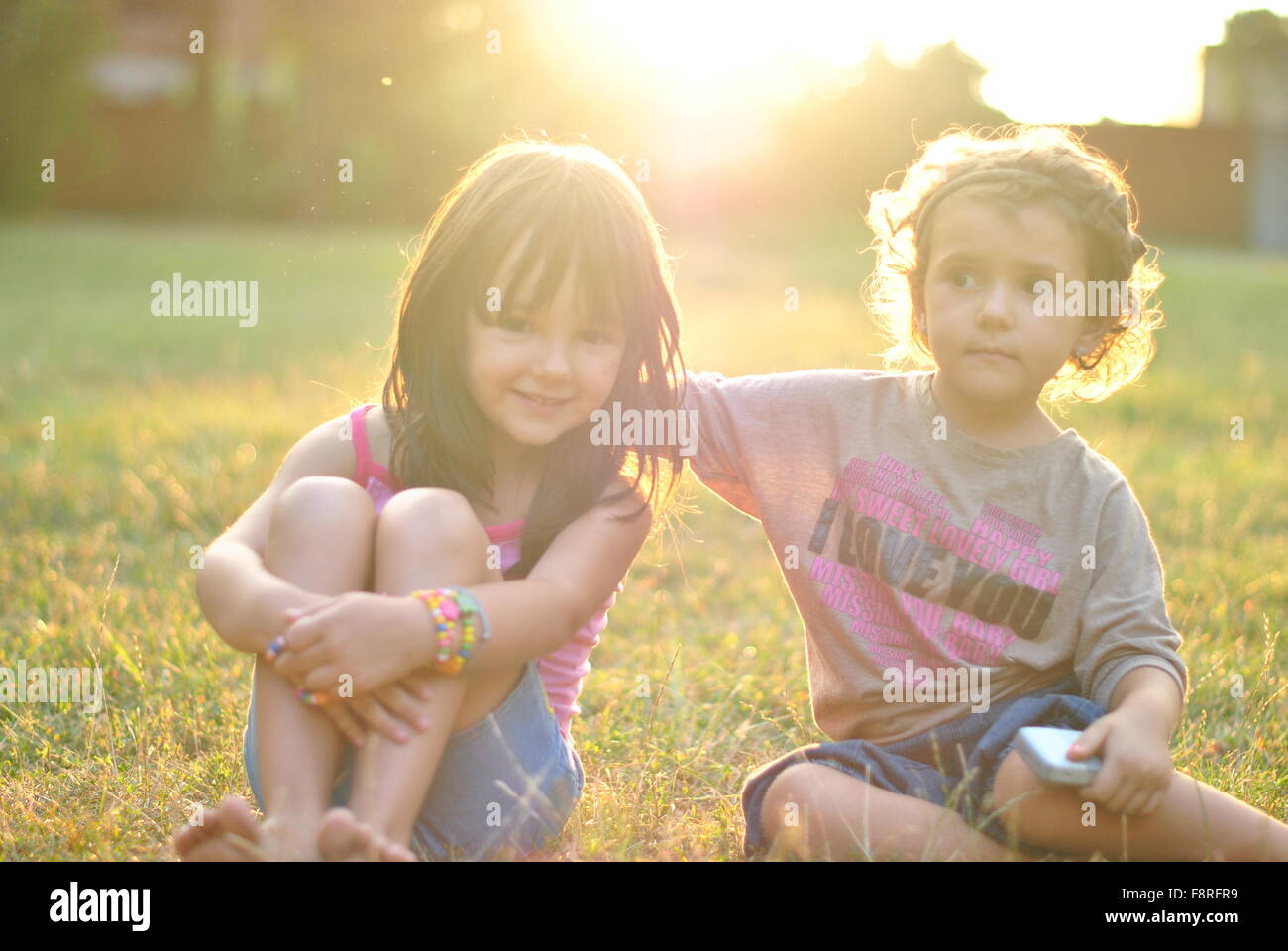 Portrait of two girls sitting in field at sunset Stock Photo - Alamy