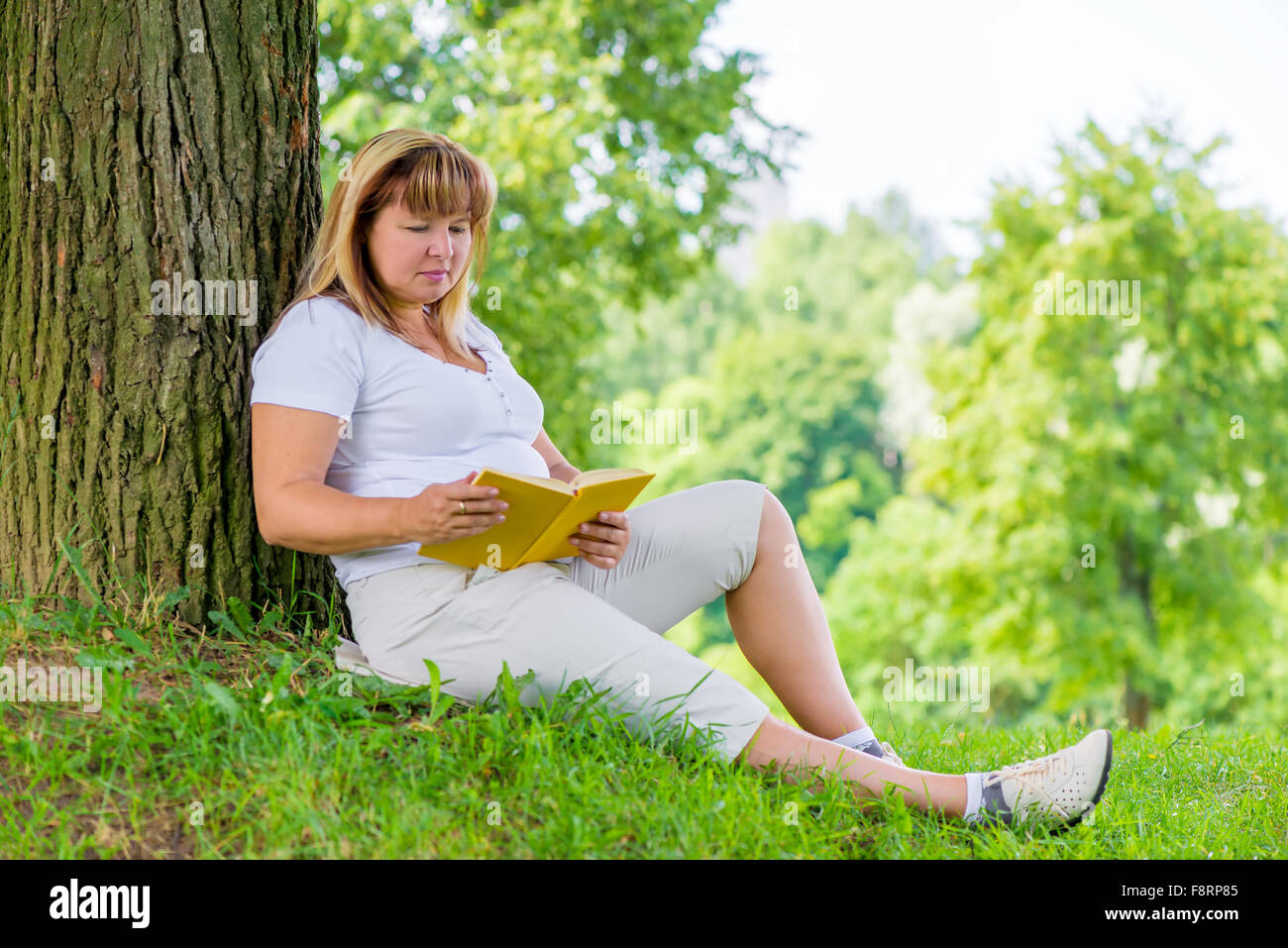 mature woman of 50 years old reading a book on the lawn in the park ...