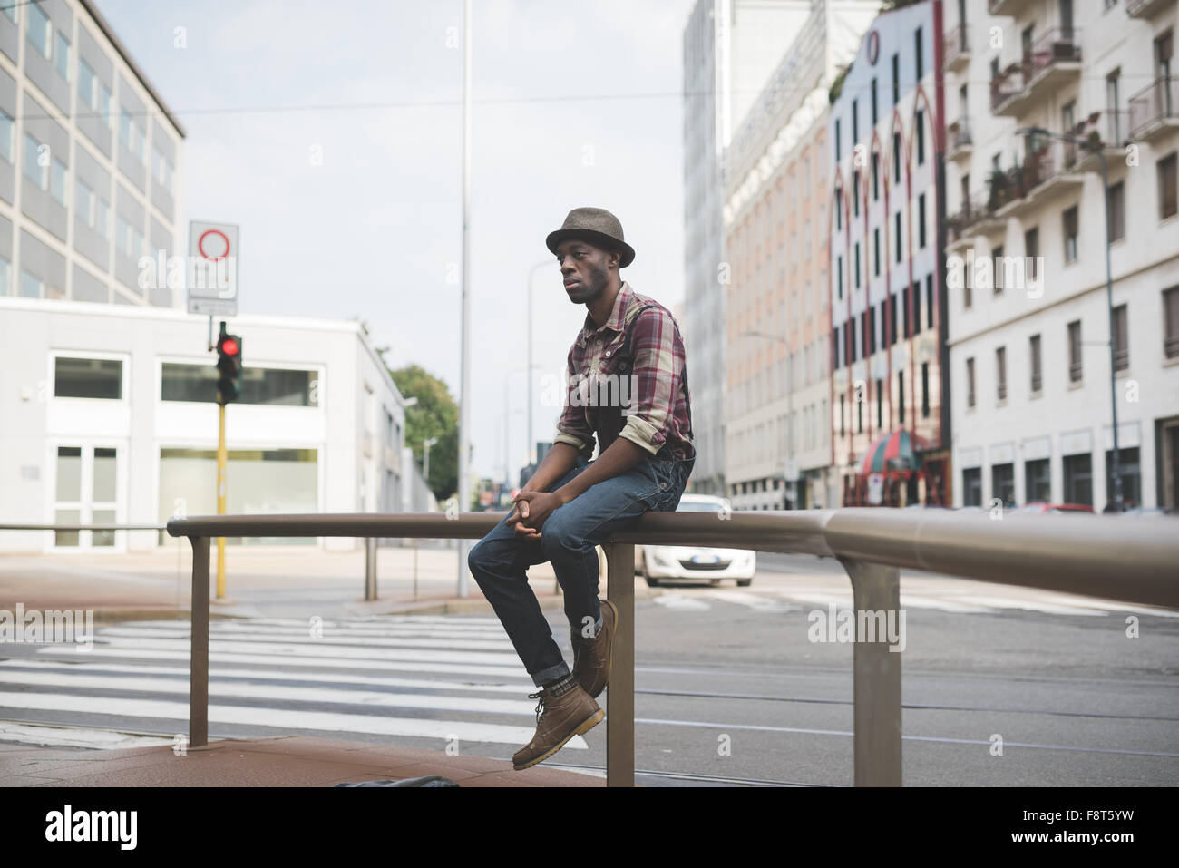 young handsome afro black man sitting on a handrail outside in the city, looking straight right ...