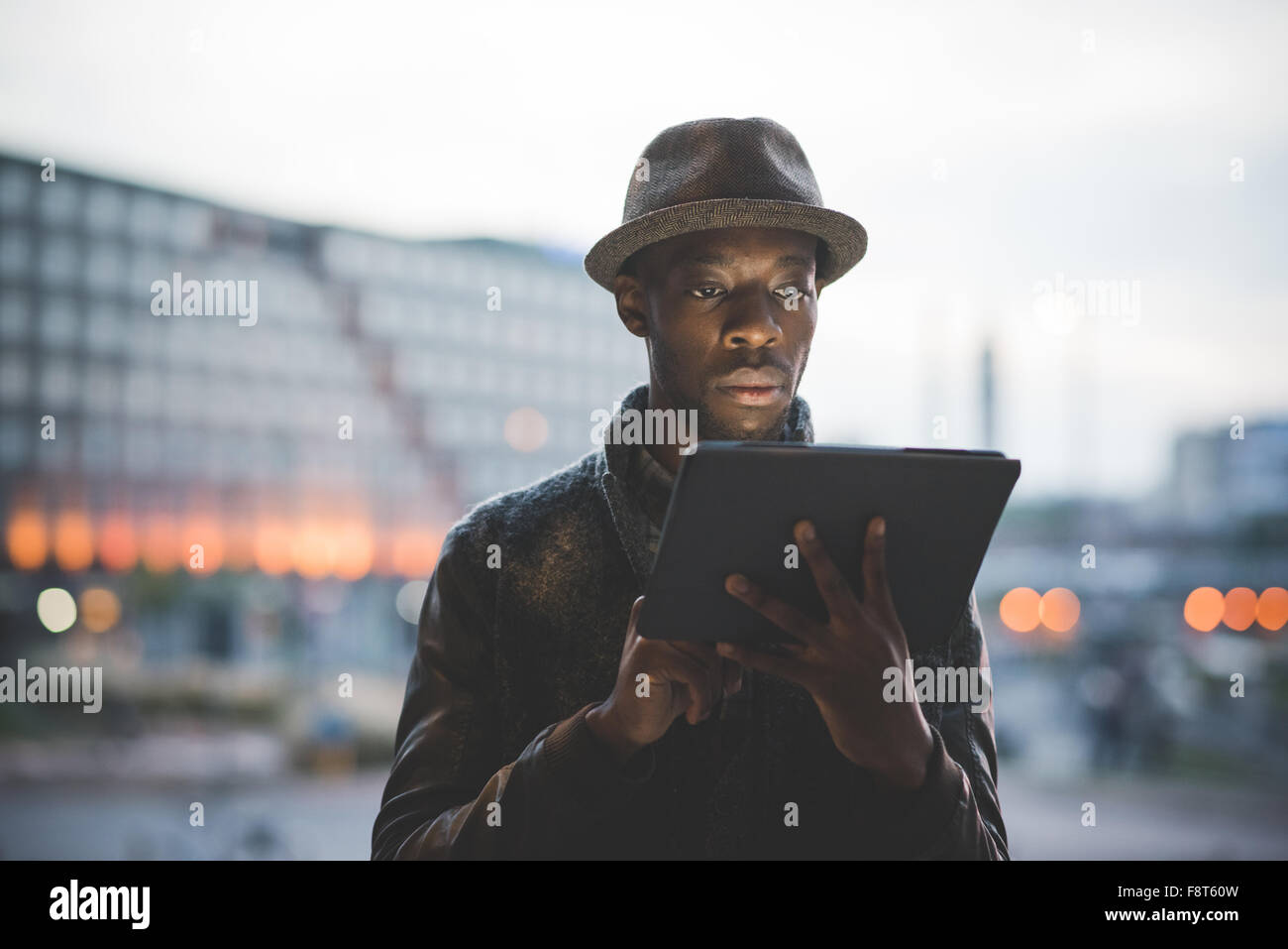 Half length of young handsome afro black man using a tablet, looking downward the screen ...