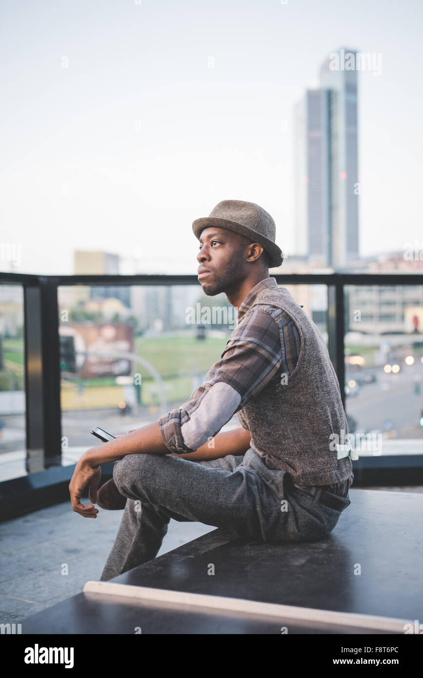 young handsome afro black man sitting with smartphone handheld, looking left, pensive - thinking ...
