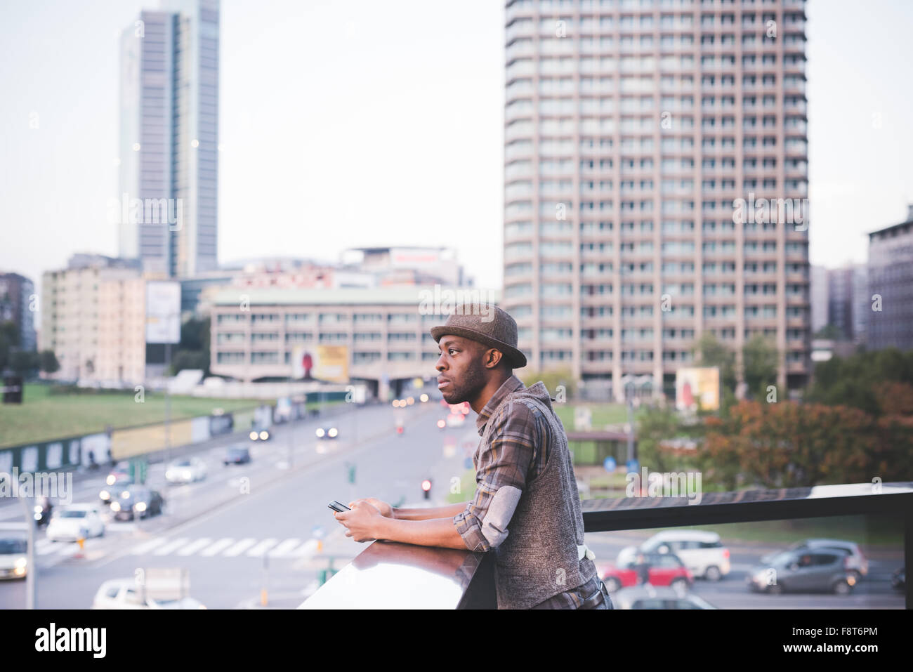 Half length of young handsome afro black man leaning against an handrail, holding a smartphone ...