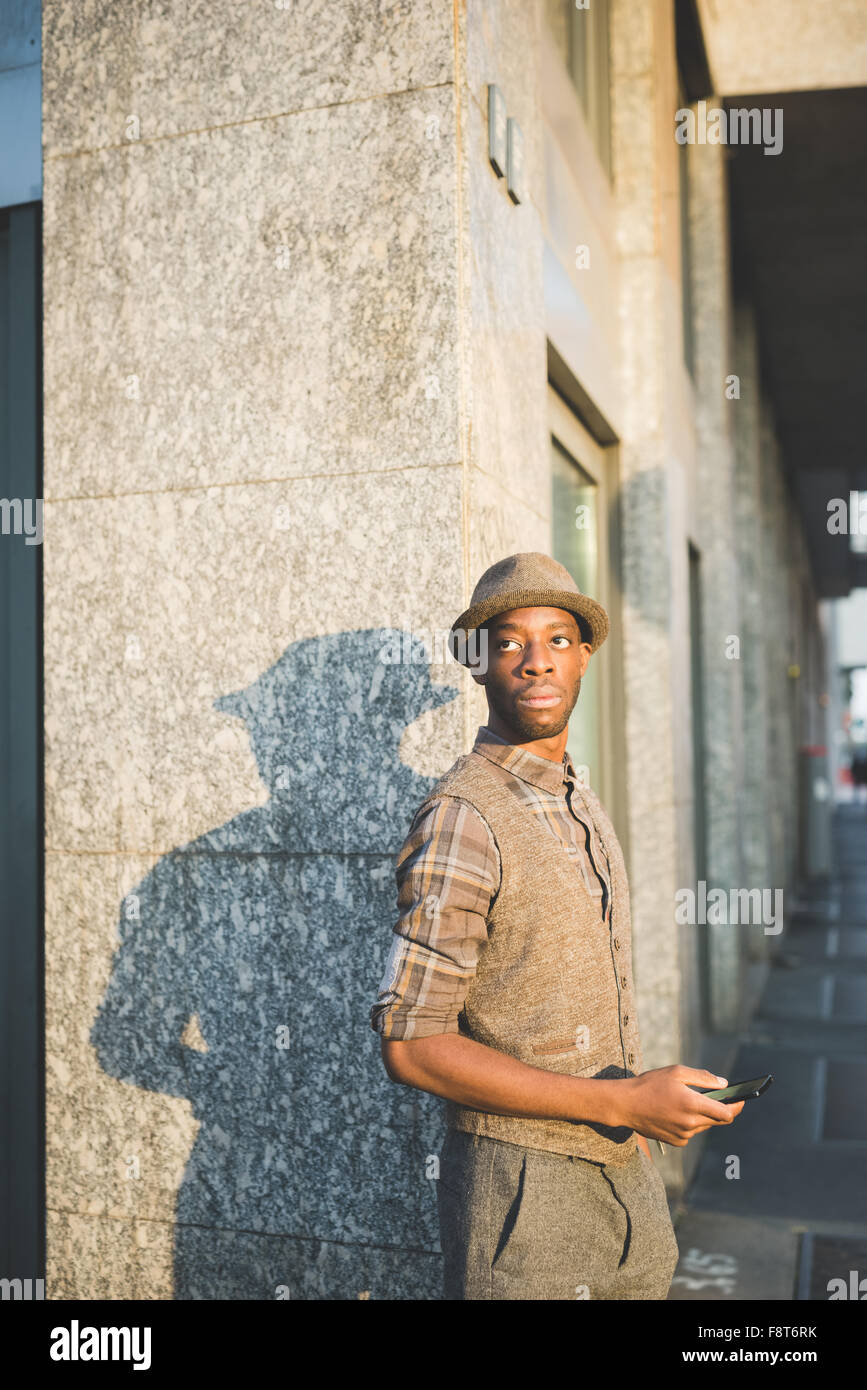 Knee figure of young handsome afro black man posing leaning against a wall, holding a smartphone ...