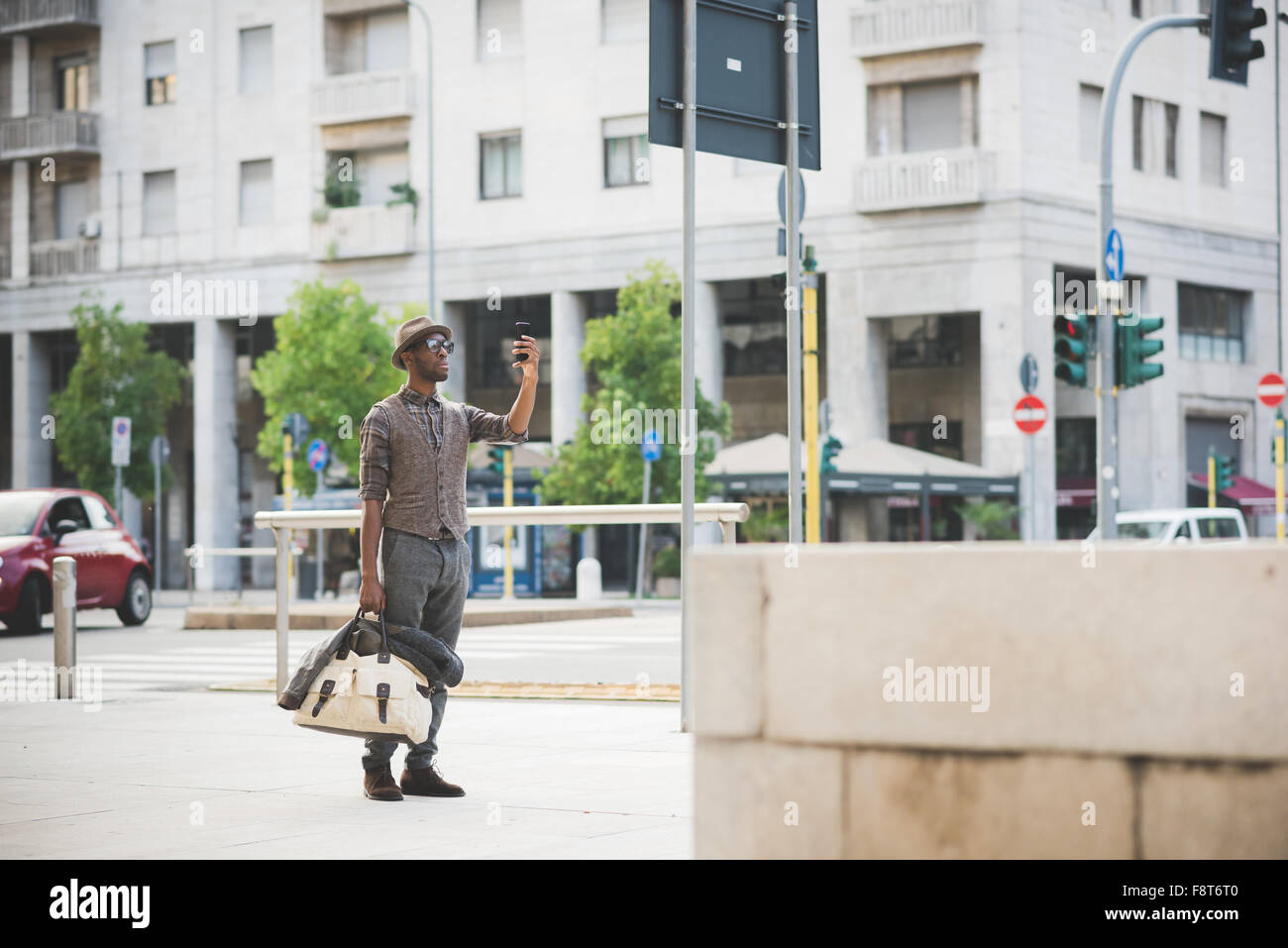 young handsome afro black man standing in the street of the city holding a bag, taking a photo ...