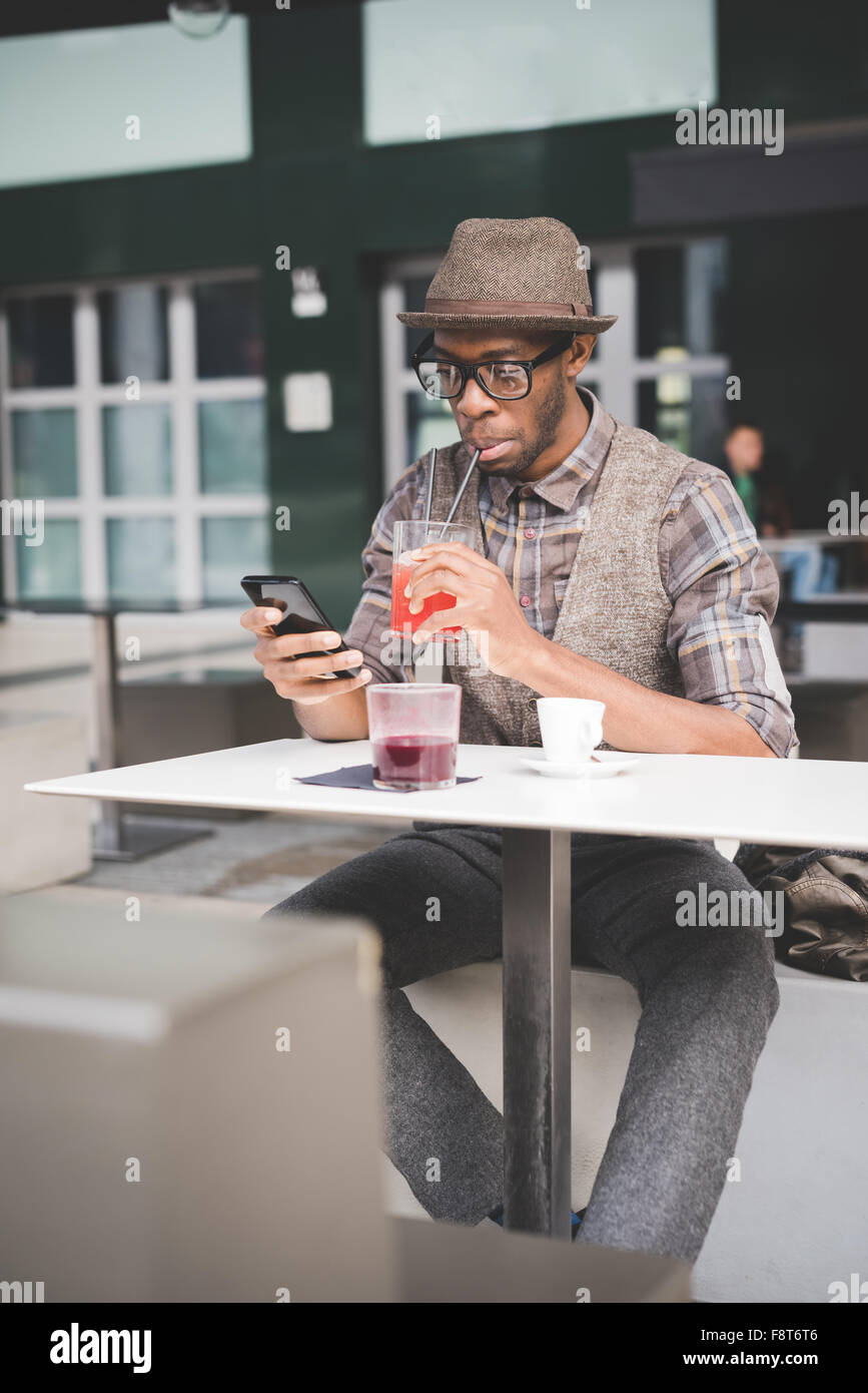 young handsome afro black man sitting on a table, smartphone handhold, looking down the screen ...