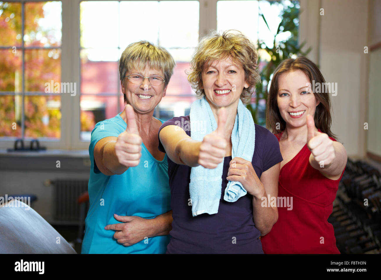 Three happy women holding thumbs up in gym Stock Photo - Alamy