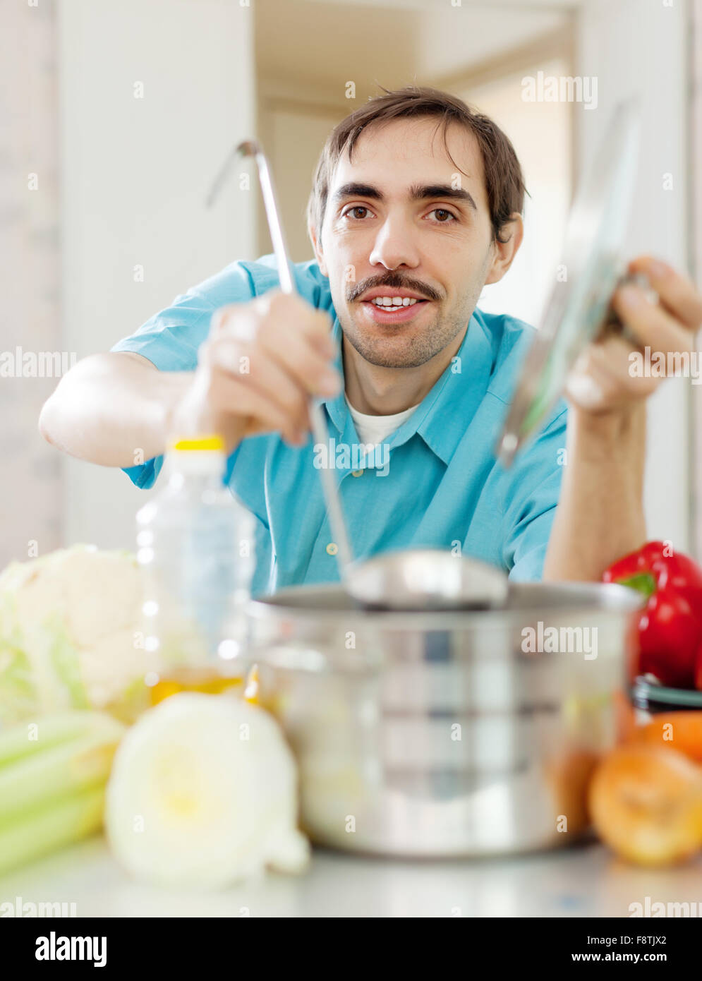 caucasian handsome guy with ladle cooking vegetables soup at kitchen ...