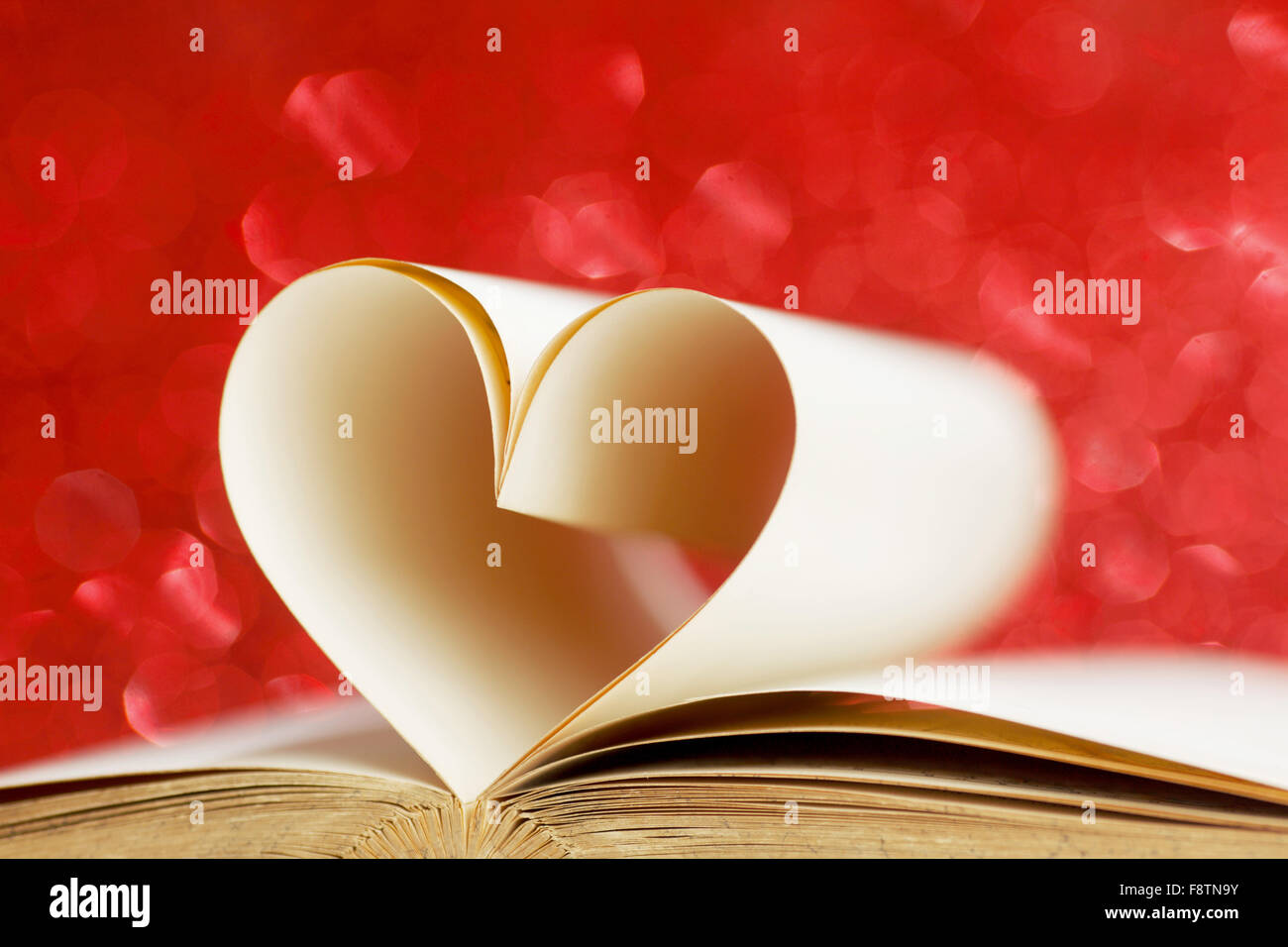 Pages of open book rolled in heart shape on glitter background Stock ...