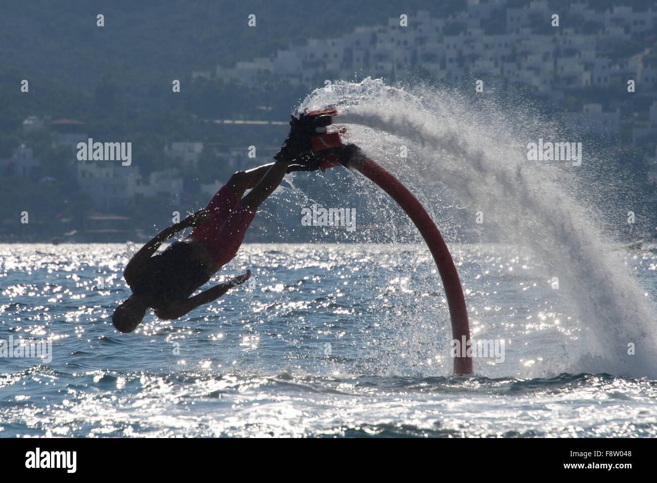 Flyboarder diving diagonally headfirst into backlit waves Stock Photo ...