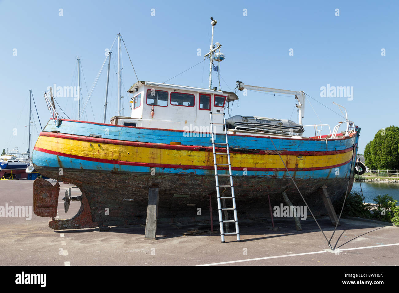 An old pale blue and yellow timber tug fishing vessel boat on stilts in ...