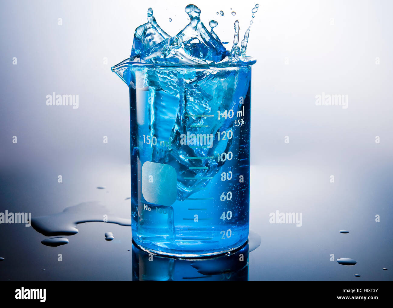 Ice falling into a laboratory glass filled with blue translucent liquid ...