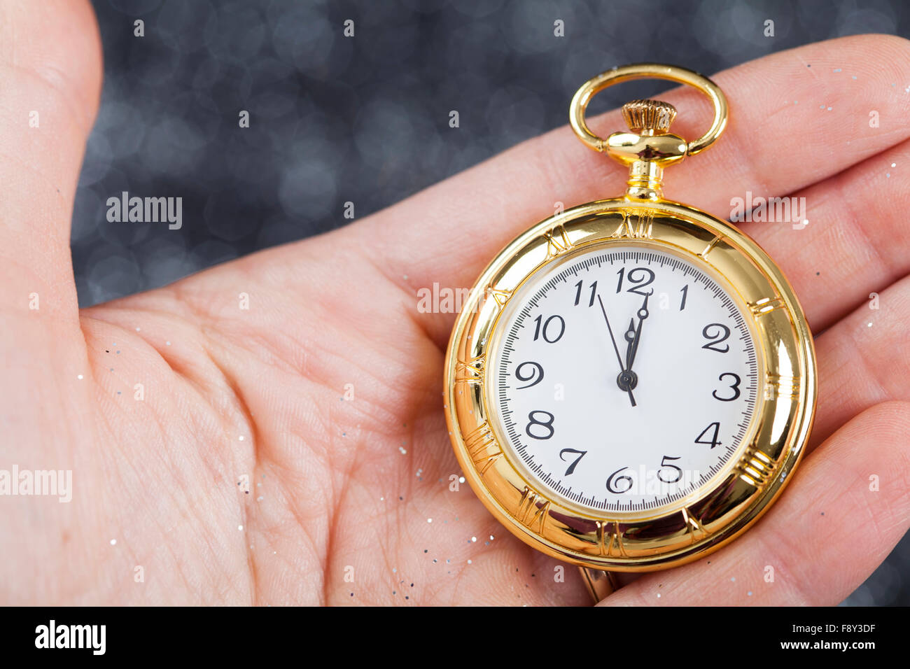 Hand holding a vintage clock closed to midnight against glittering ...