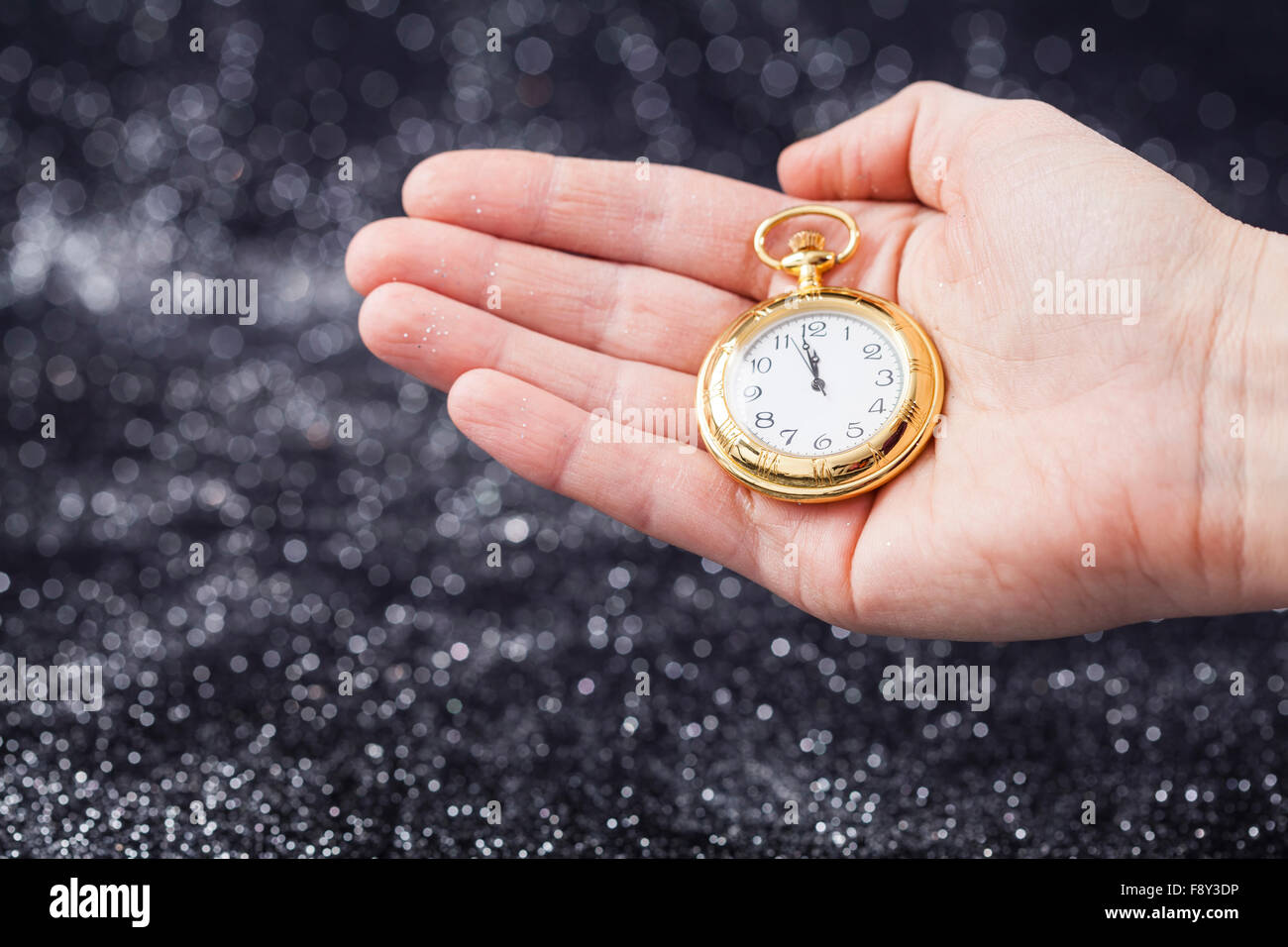 Hand holding a vintage clock closed to midnight against glittering ...