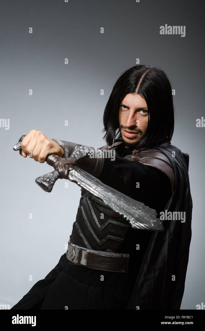 Angry knight with sword against dark background Stock Photo - Alamy