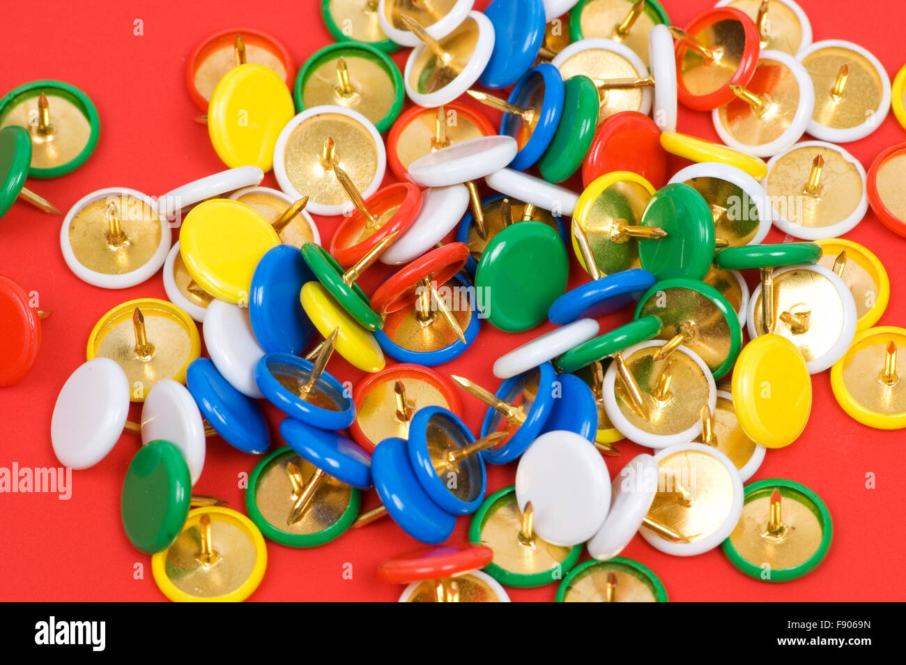 Many colourful office pins on red background Stock Photo - Alamy
