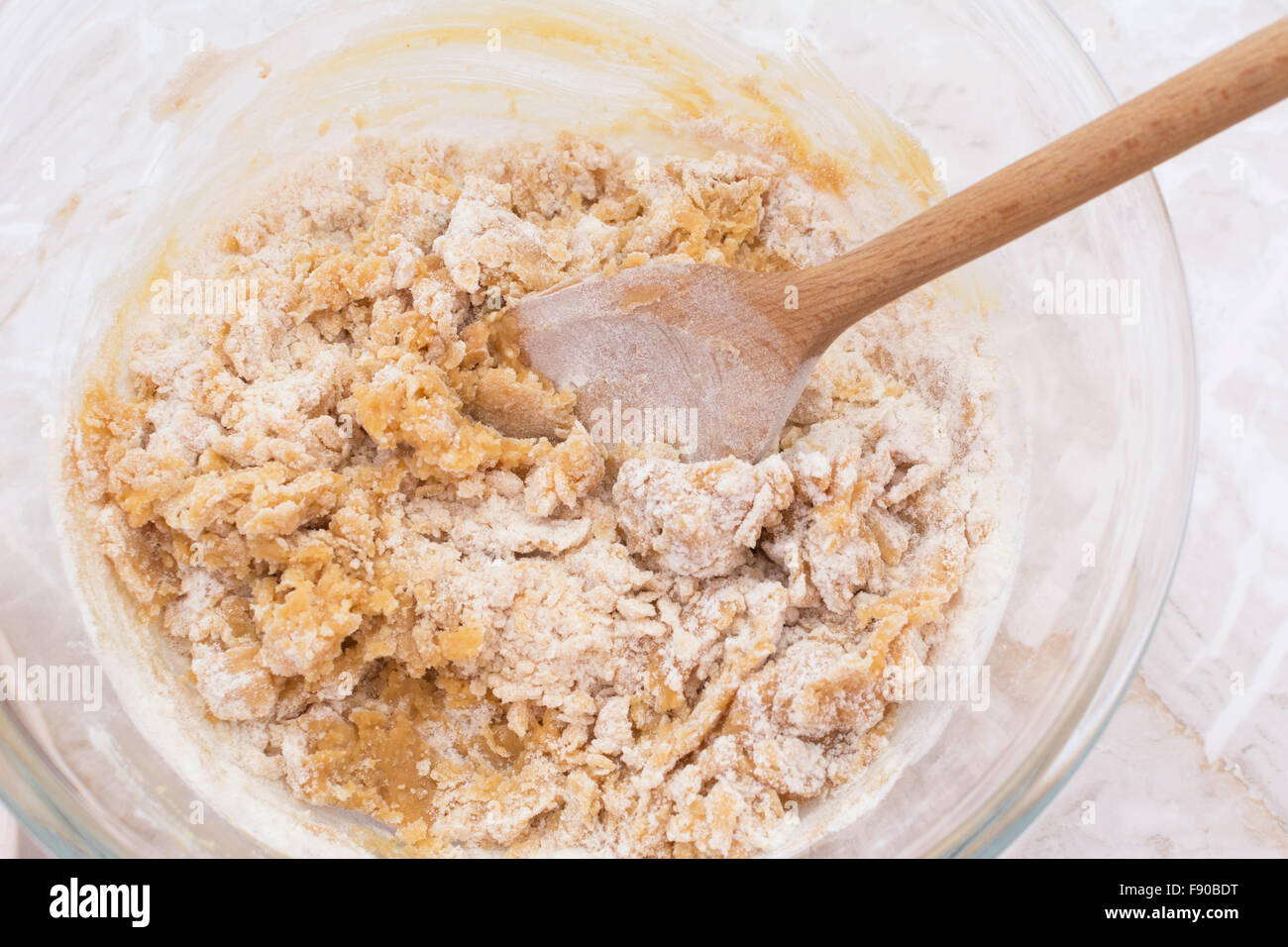 Stirring cookie dough together with a wooden spoon to make peanut ...
