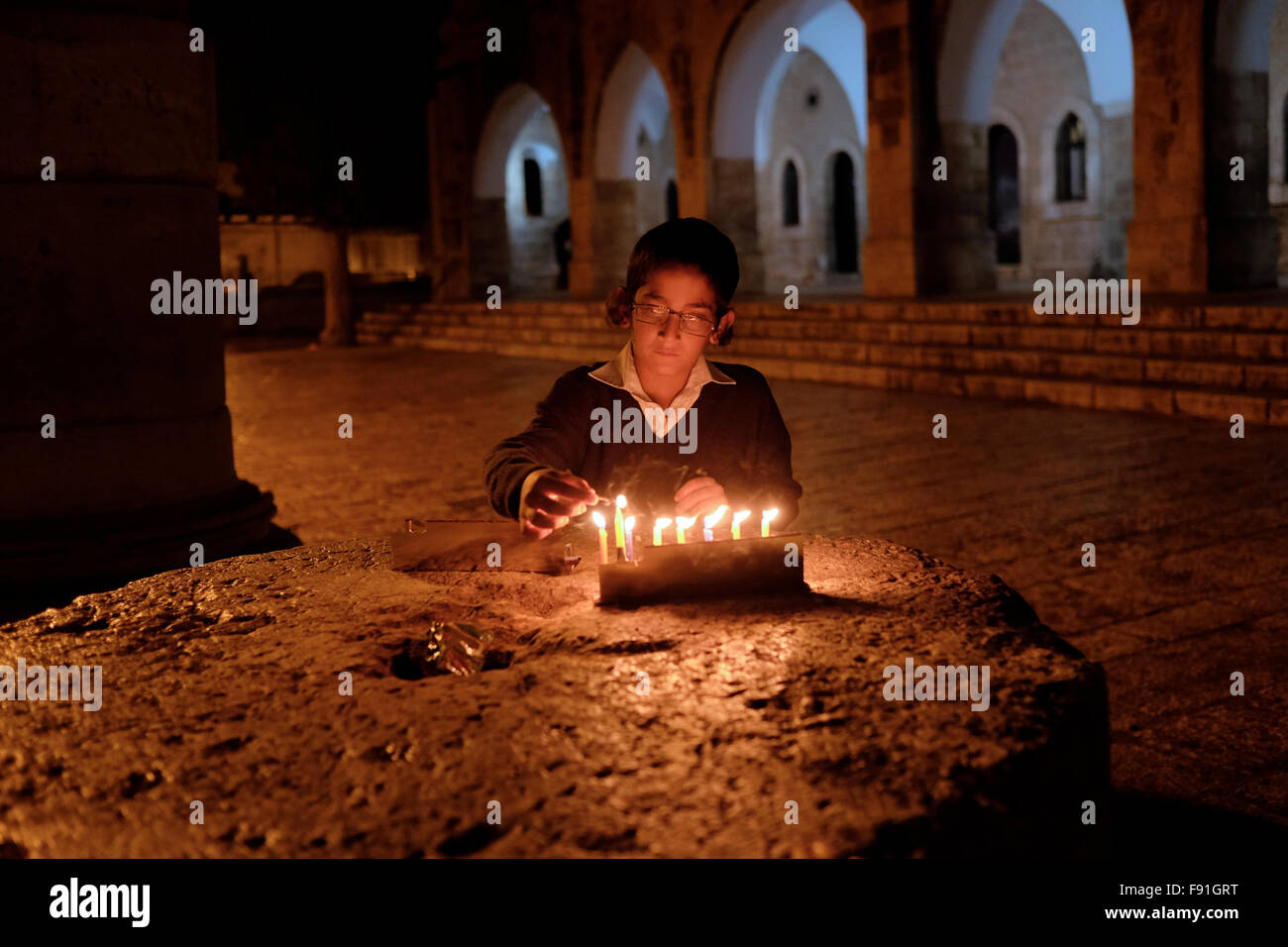 Young religious Jewish boy lights a candle on a menorah on the 8th day ...