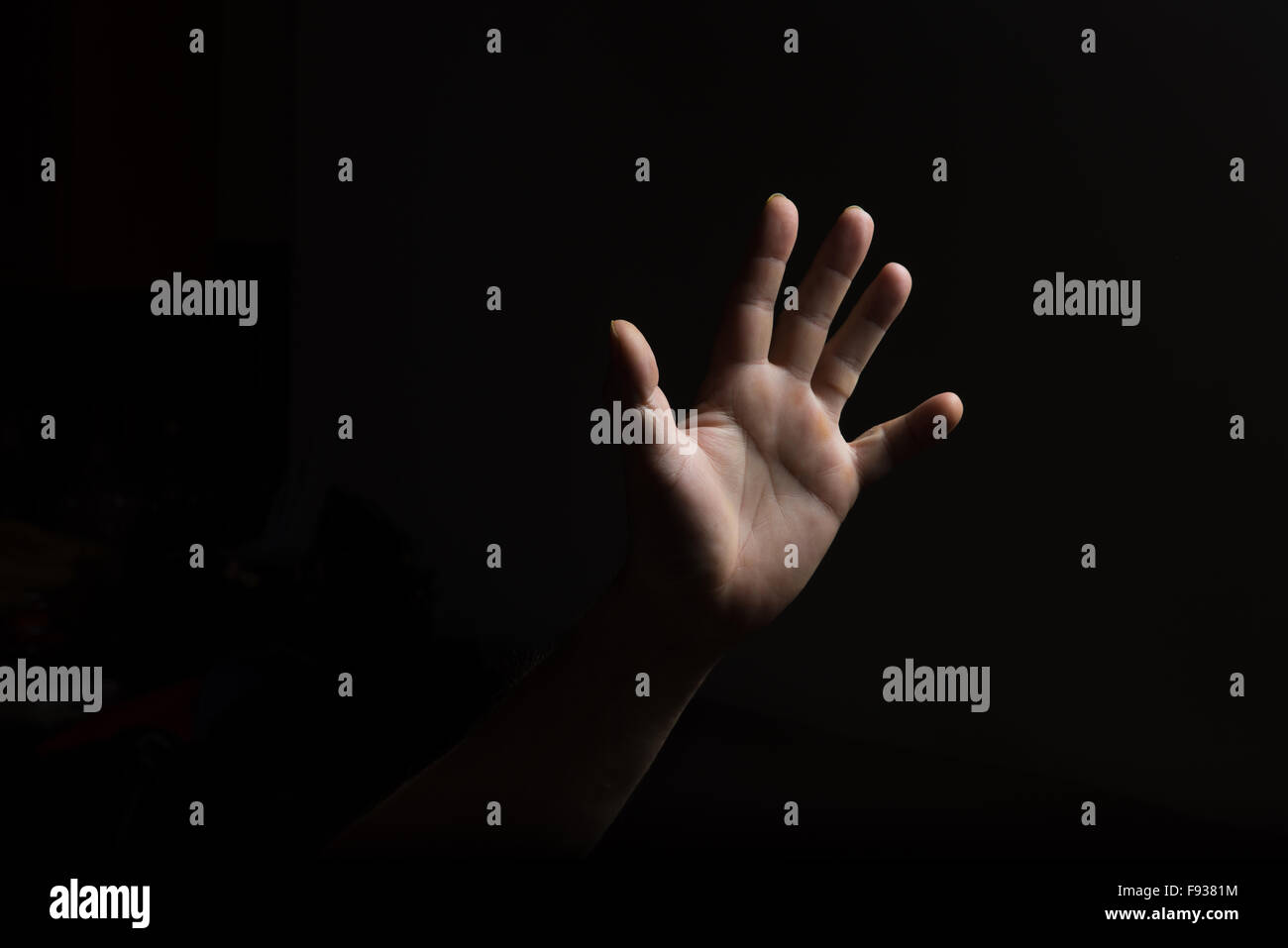 A mans hand reaching up against a black background Stock Photo - Alamy