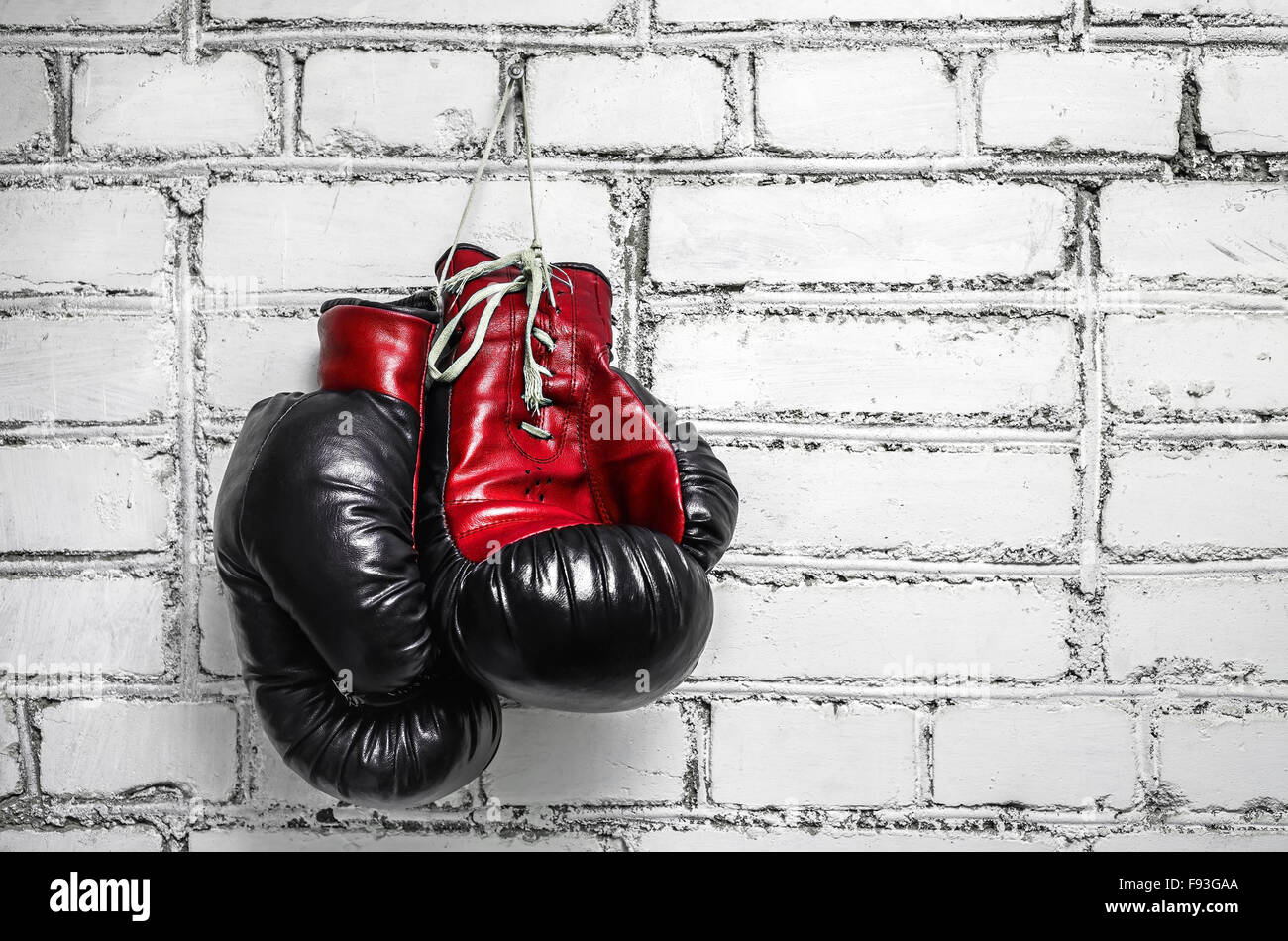 A pair of old boxing gloves hanging against a white brick wall Stock ...